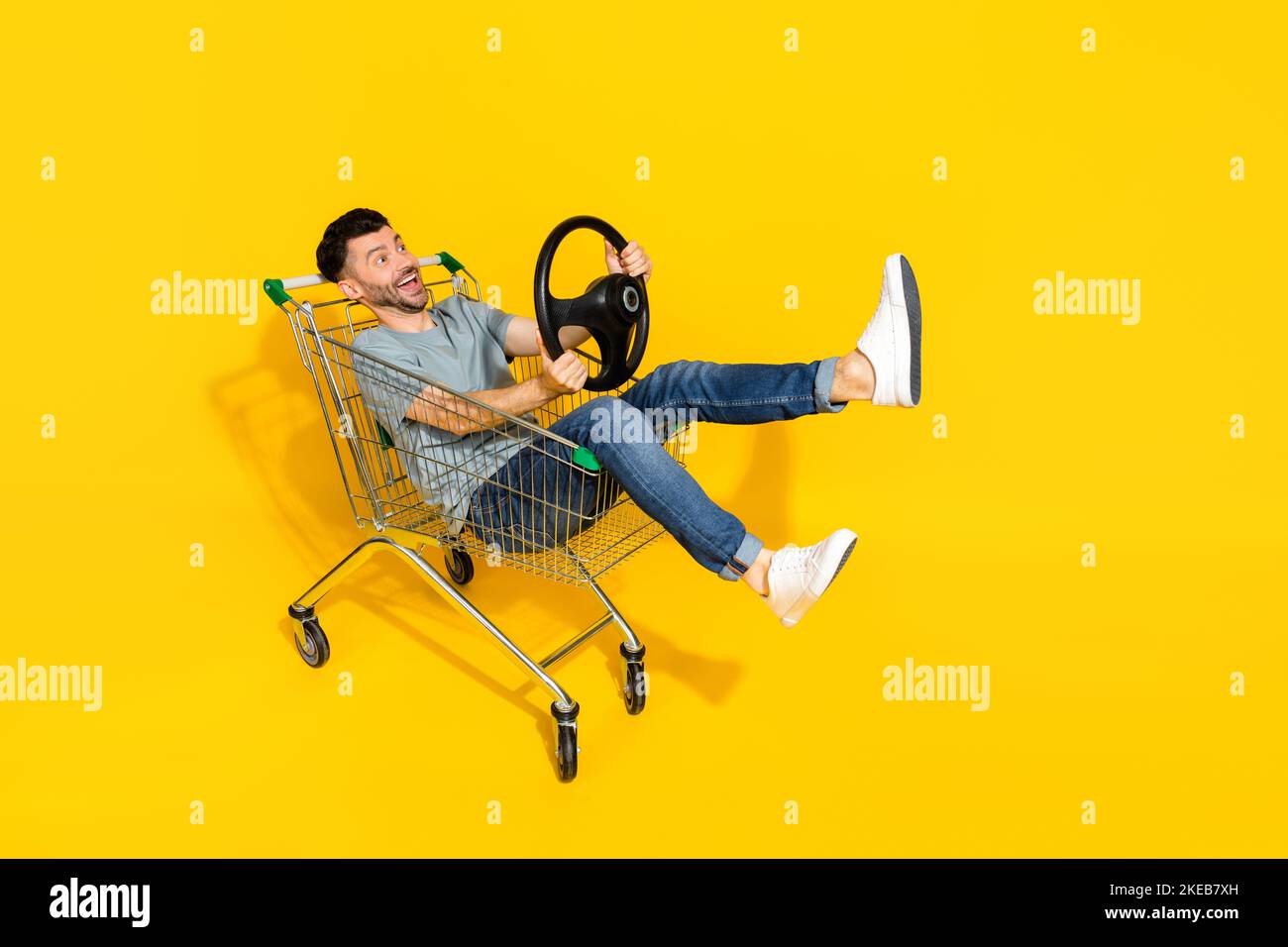 Full body photo of excited positive guy sit market trollet arms hold ...