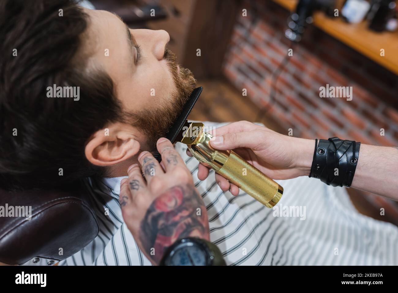 high angle view of tattooed barber trimming beard of man with hair ...