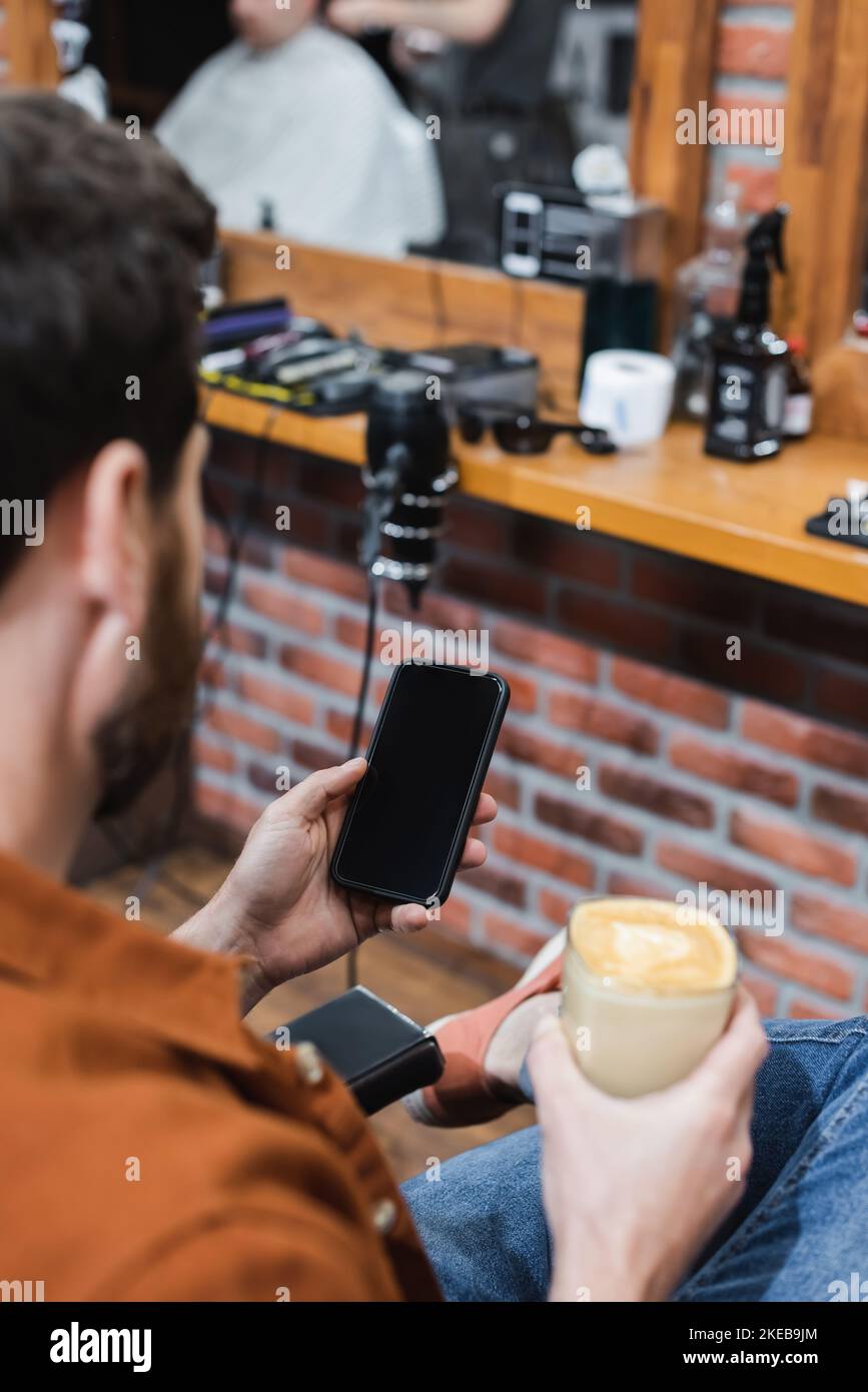 cropped view of blurred client with glass of cappuccino holding ...