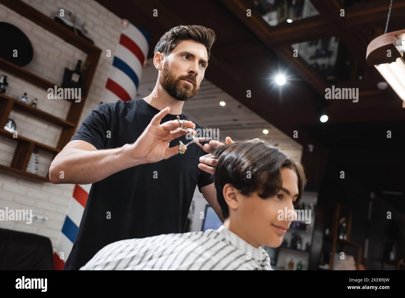 low angle view of bearded barber doing haircut to teenage client in ...