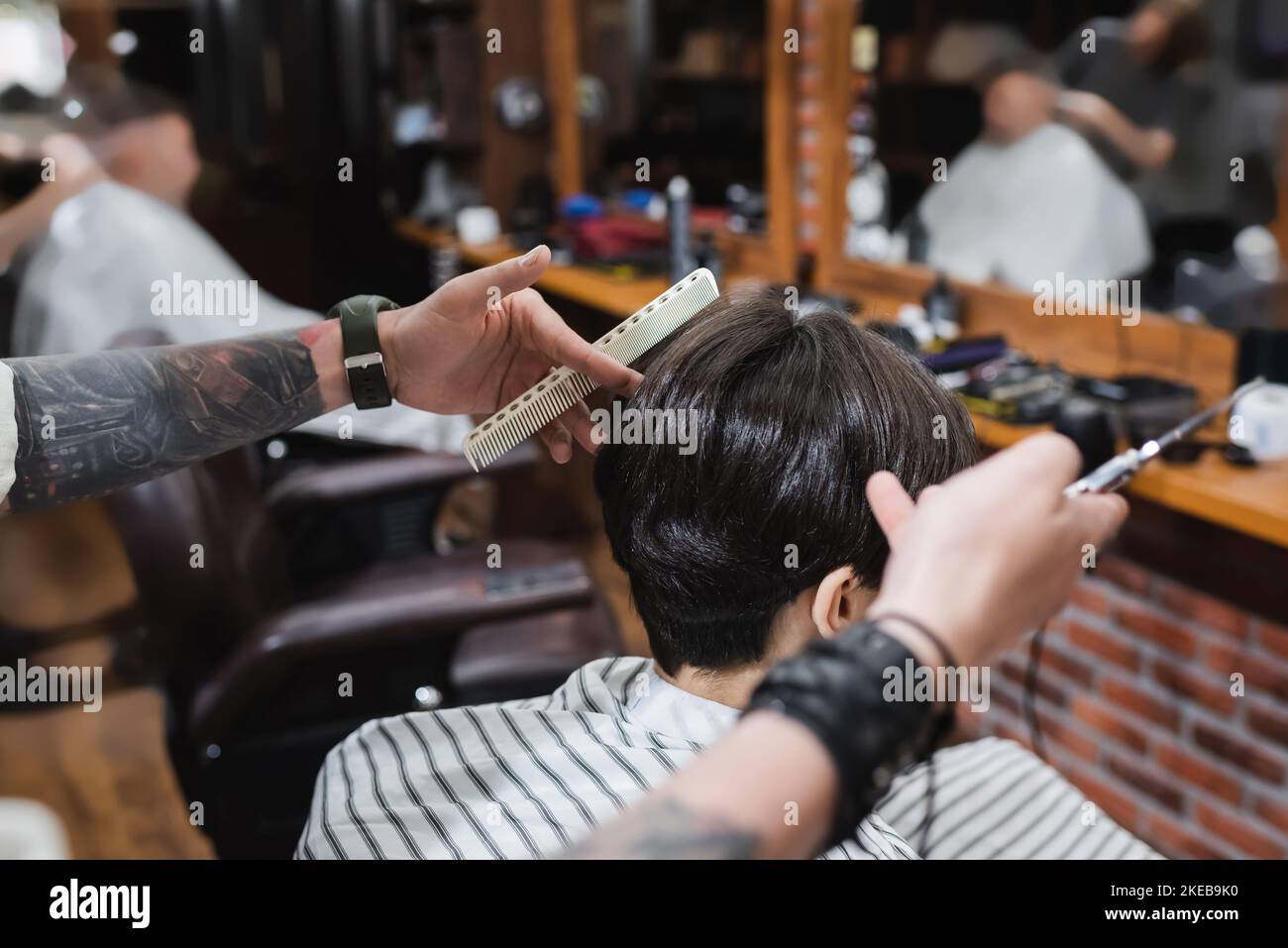 tattooed barber with comb and blurred scissors near brunette teenager ...