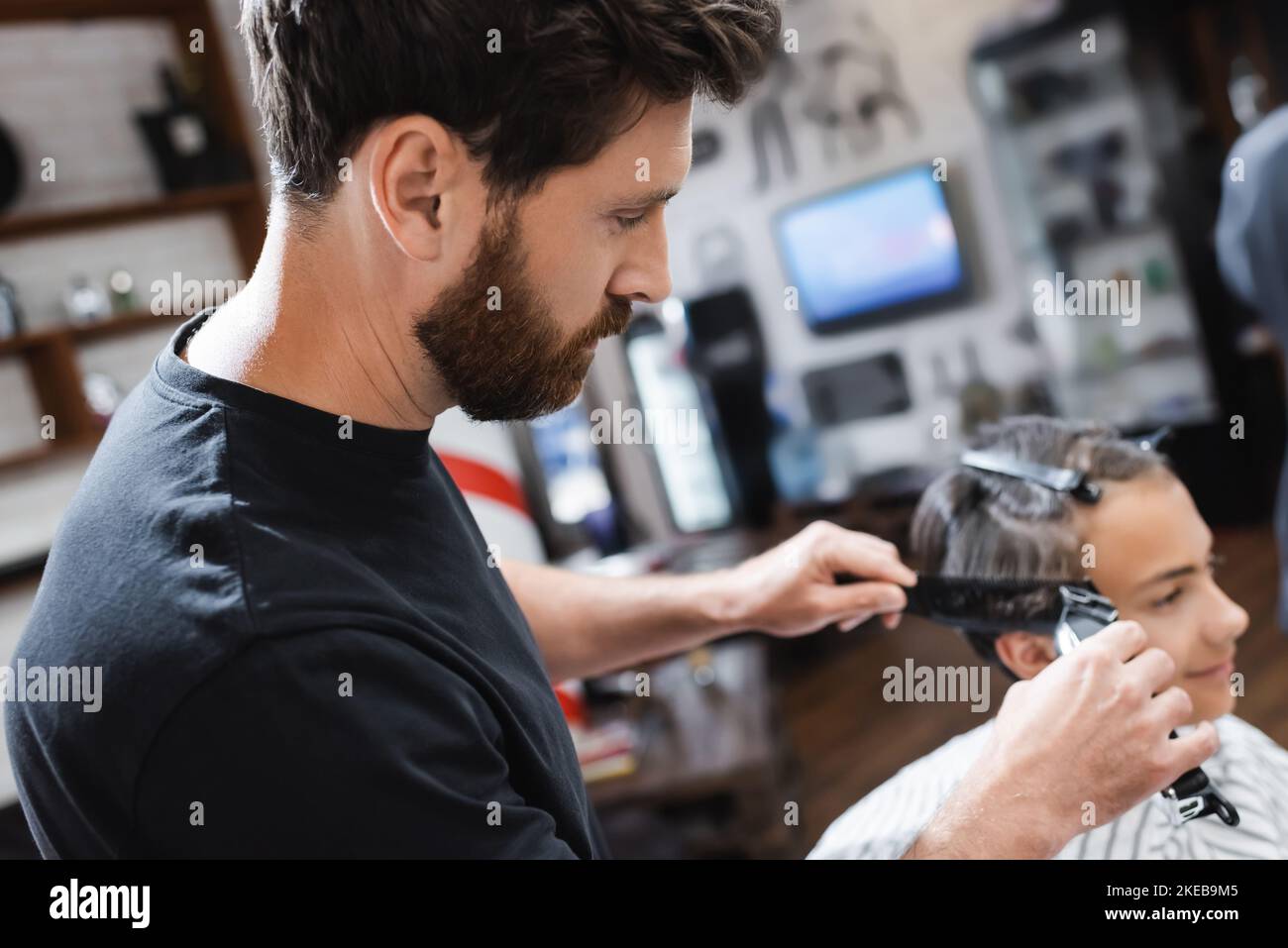 Hairdresser holding hair clipper and comb while working with teen ...