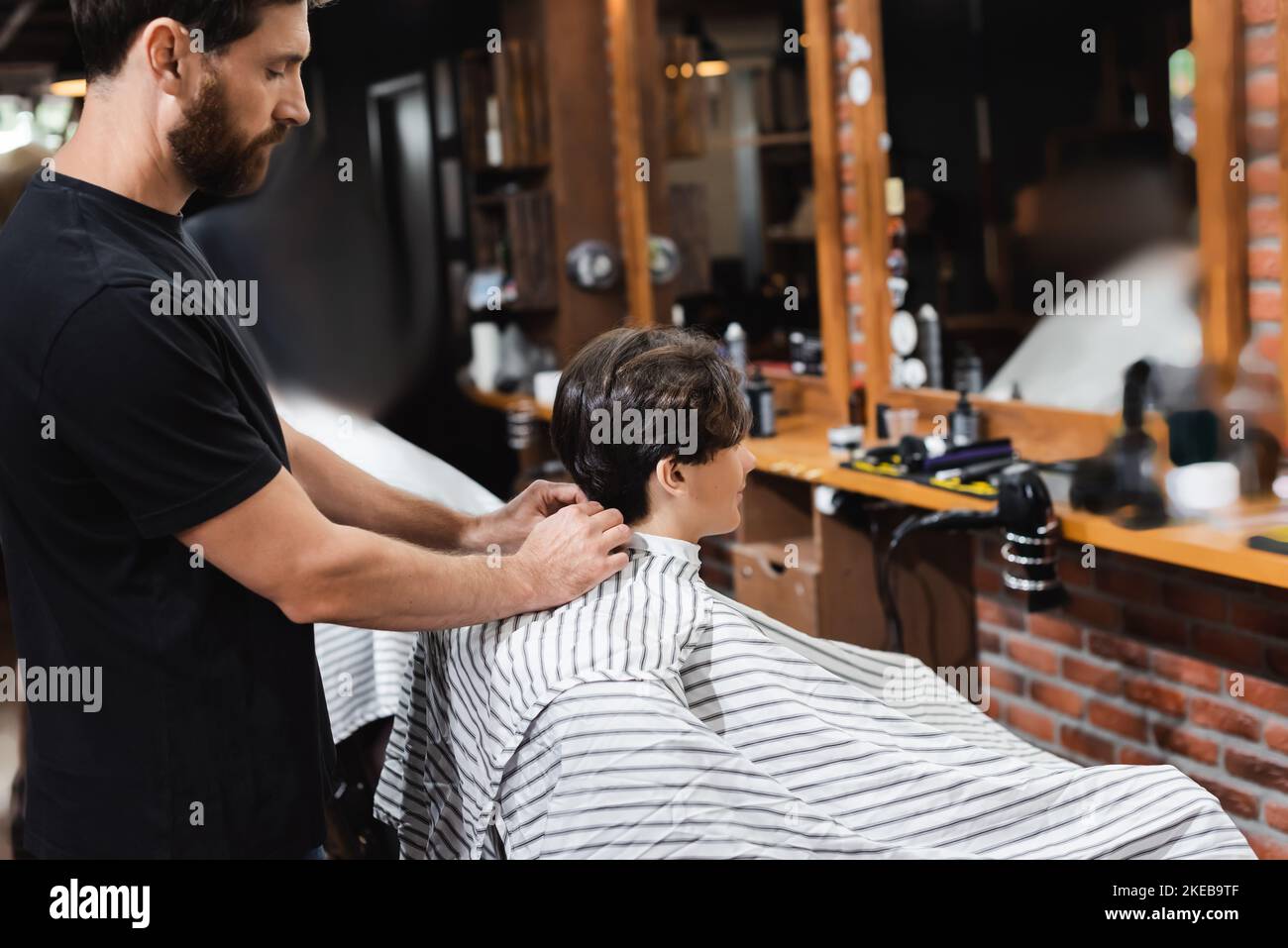 Side view of hairdresser wearing cape on teen boy in beauty salon,stock ...