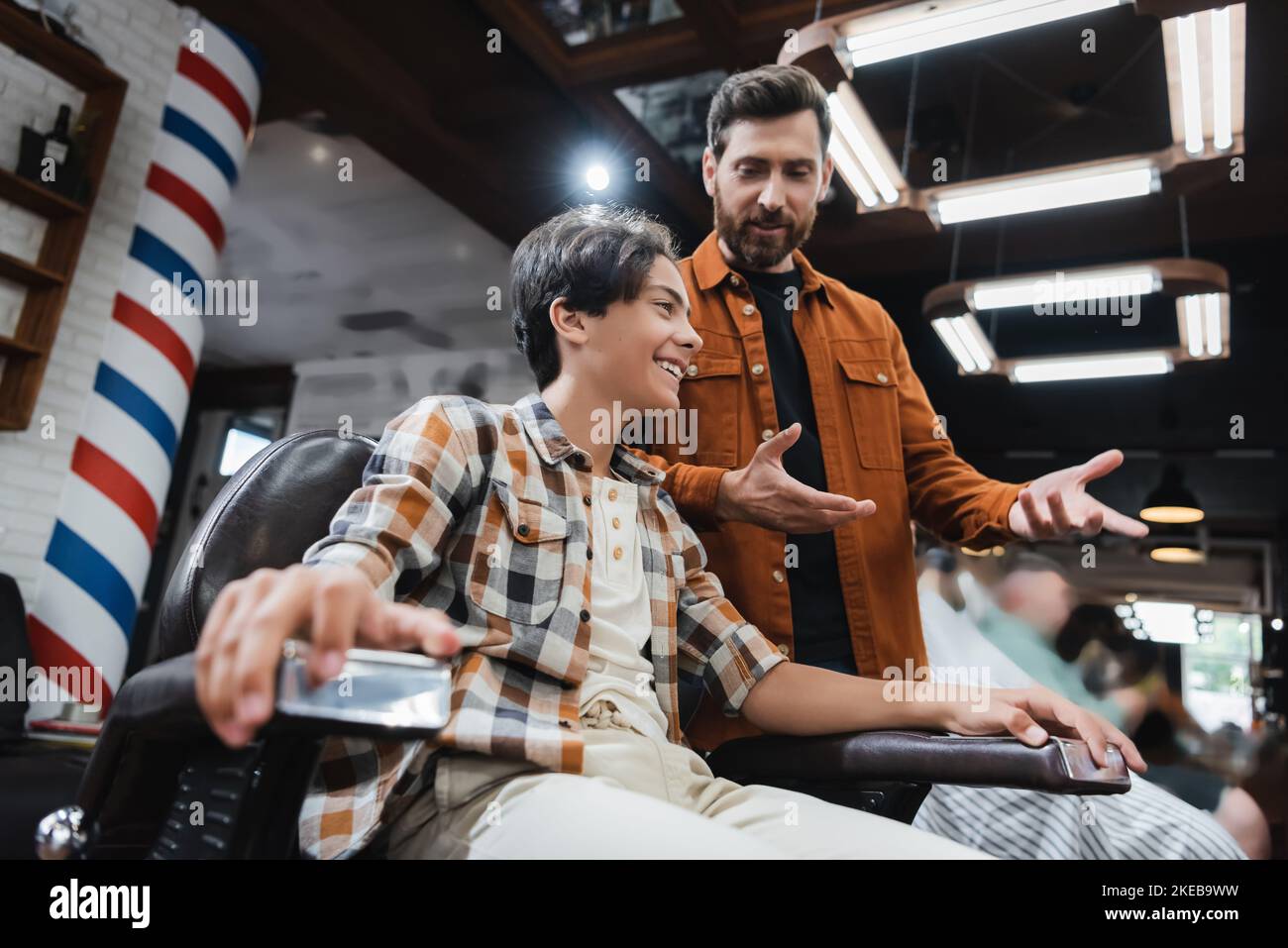 Low angle view of smiling teenage client sitting in armchair while ...