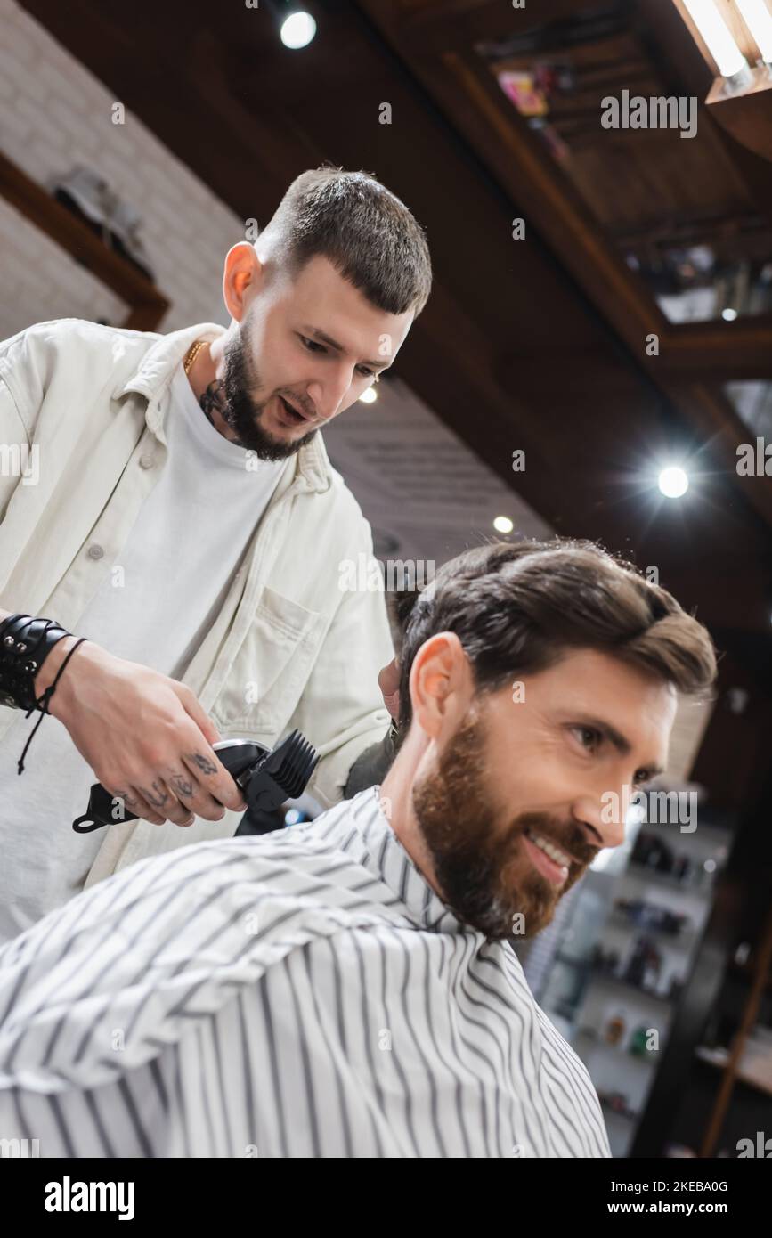 Hairstylist holding hair clipper and talking to smiling client in ...