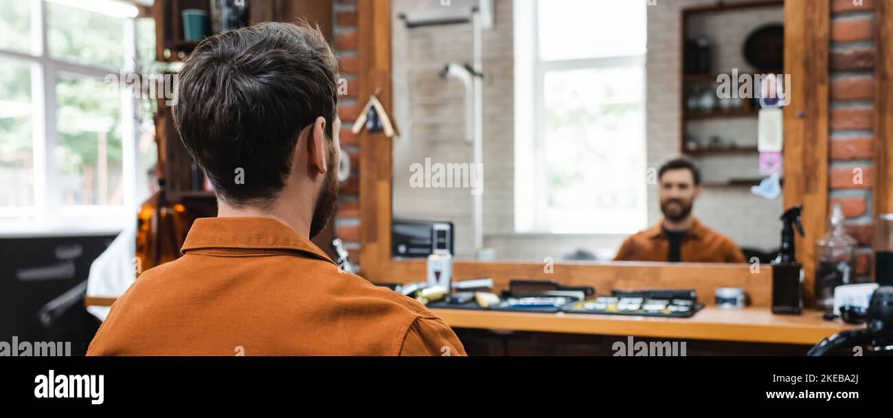 back view of brunette man sitting in barbershop near blurred mirror ...
