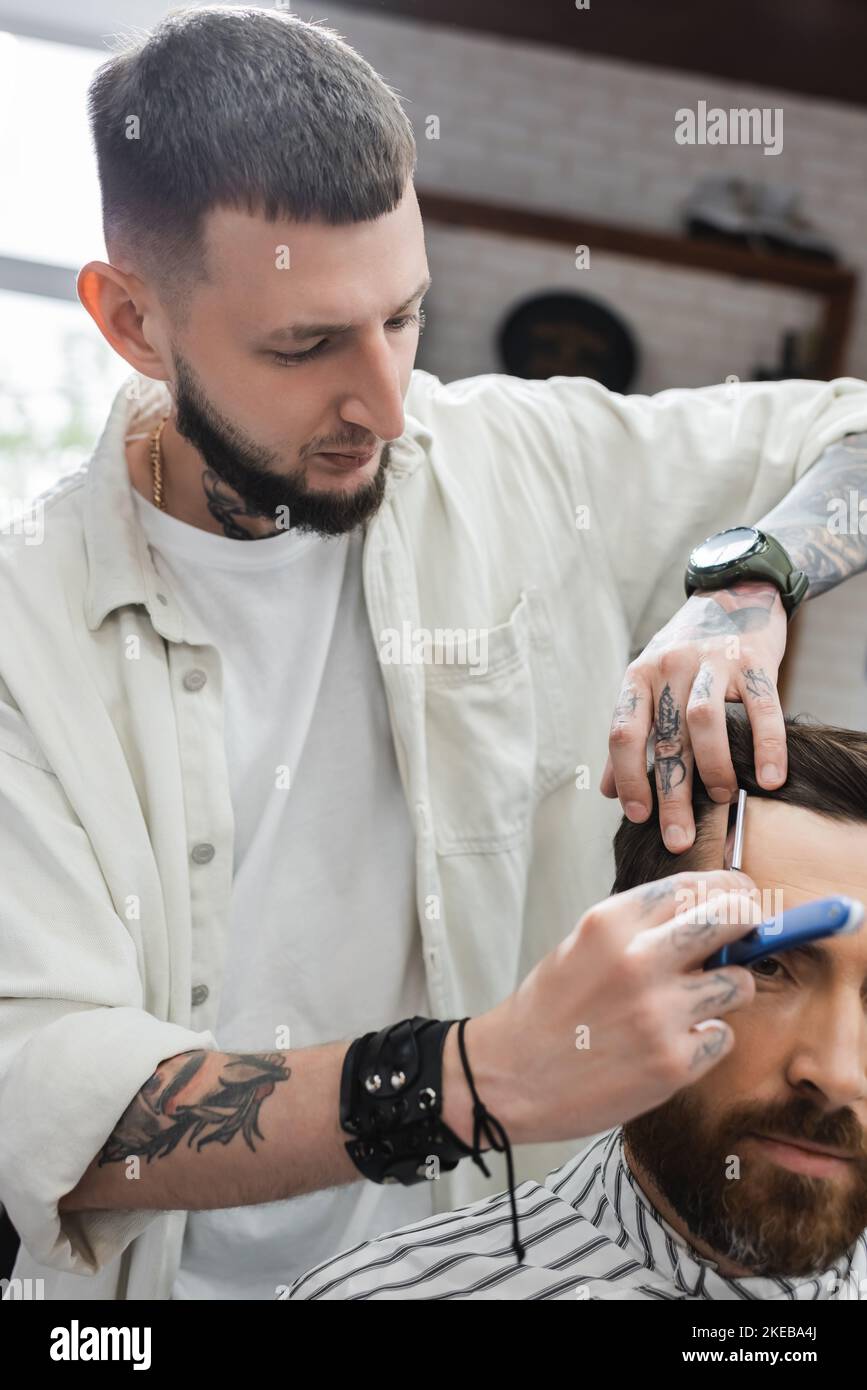 bearded barber shaving forehead of client with straight razor,stock ...