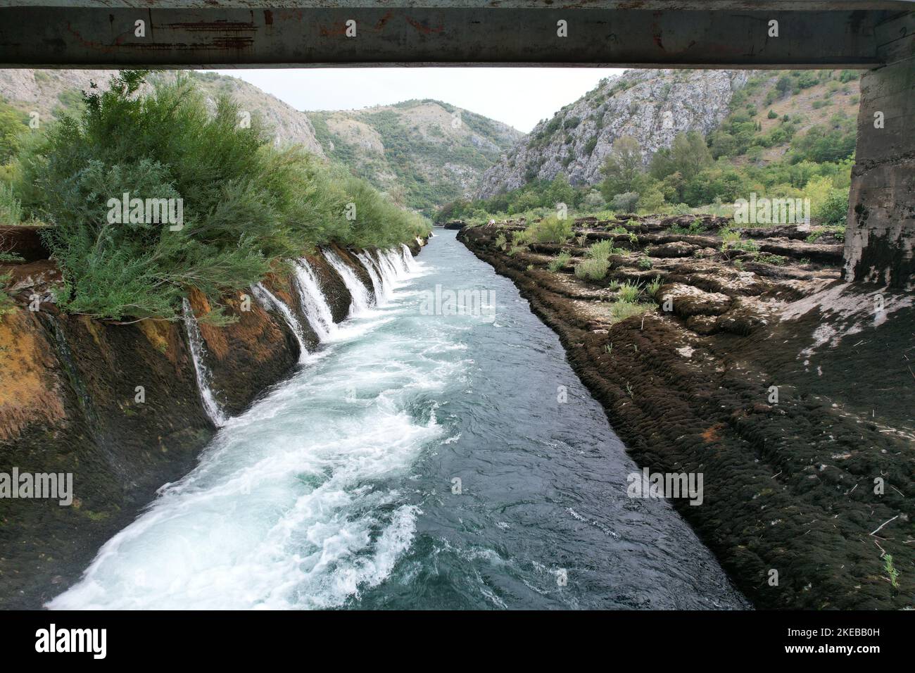A Bunski canal with water flowing from the bridge with grasses Stock ...