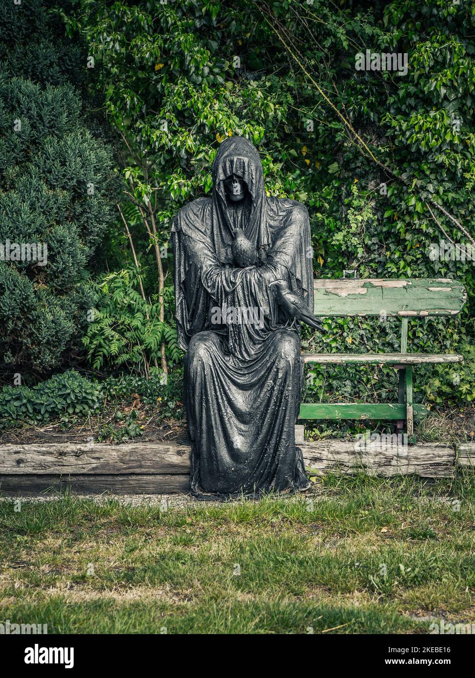 A spooky black figure sitting on a bench against a backdrop of leaves ...