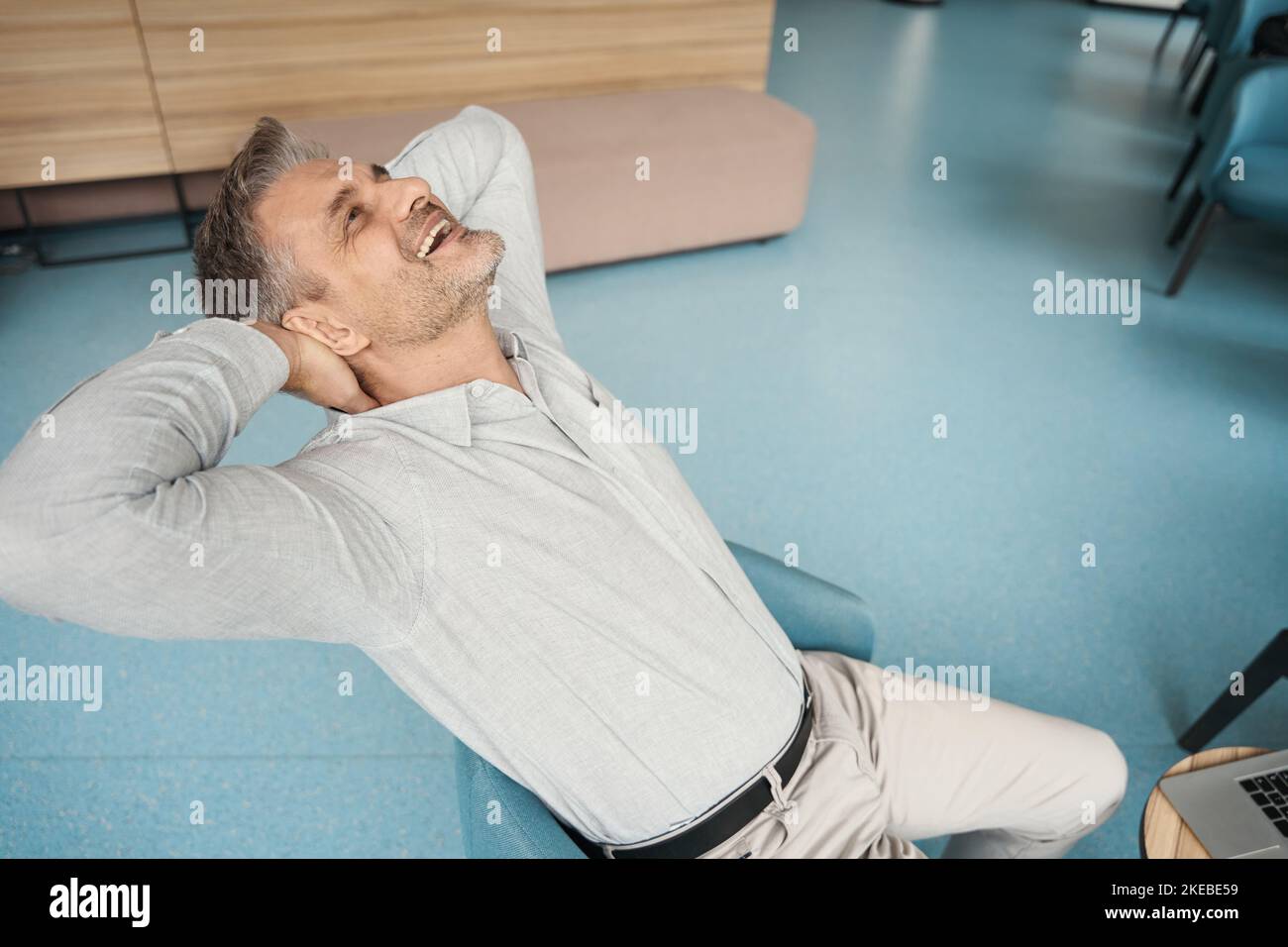 Smiling manager is resting in coworking area with comfortable furniture ...