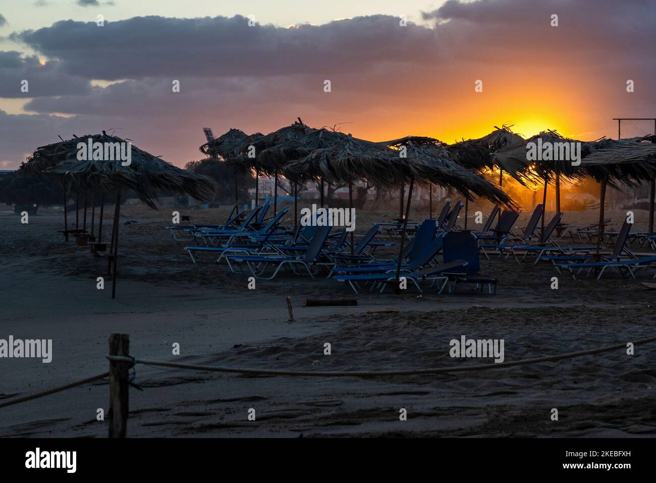 Morning sunlight illuminates dark umbrella and deckchair on beach ...