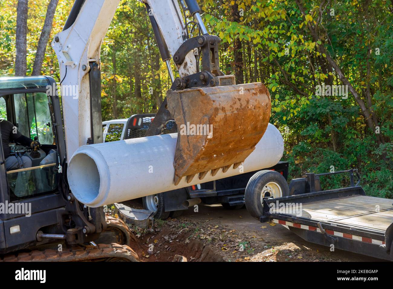 An excavation worker uses tractor to lift concrete sewage pipes from ...