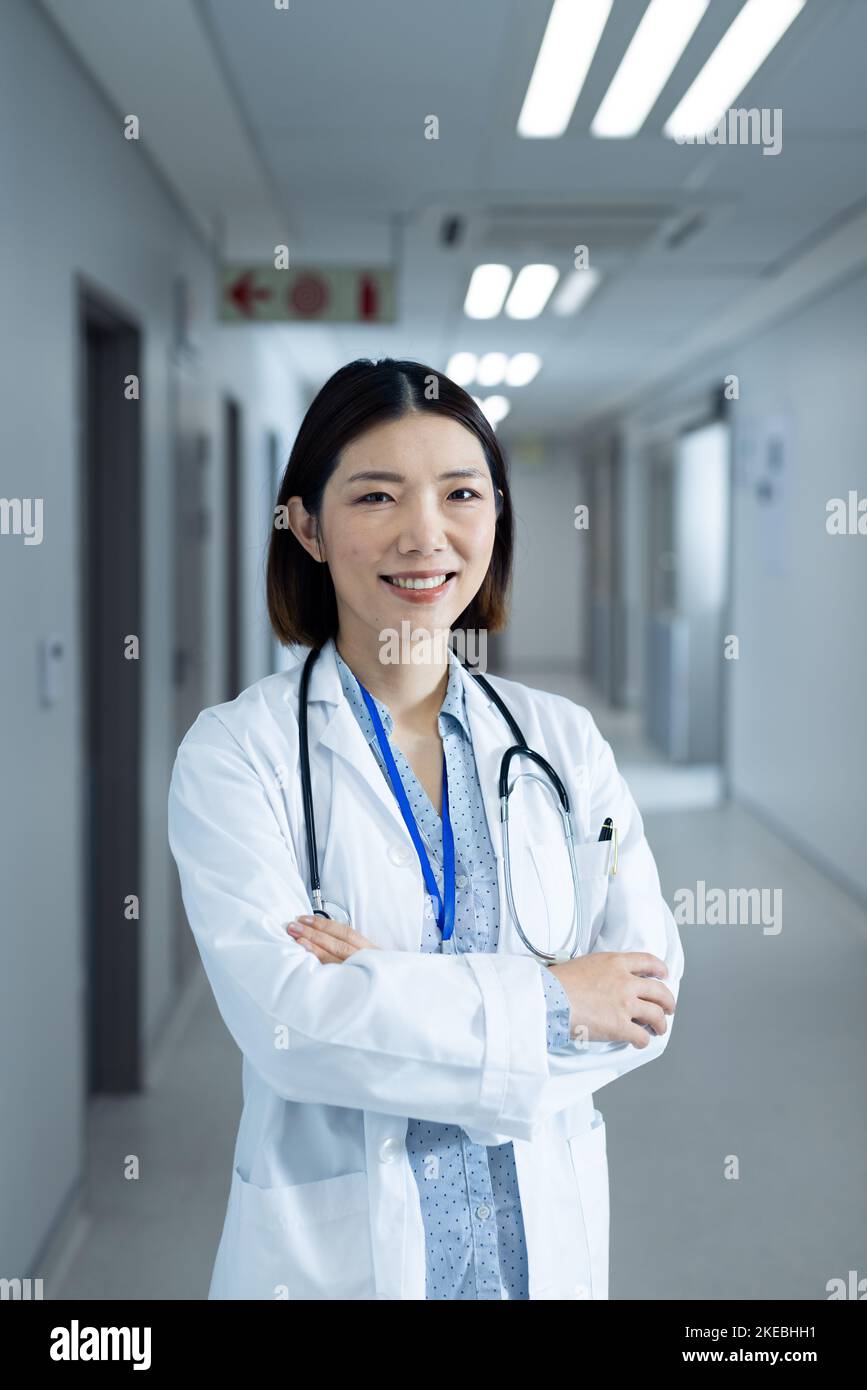 Vertical portrait of smiling asian female doctor in hospital corridor ...