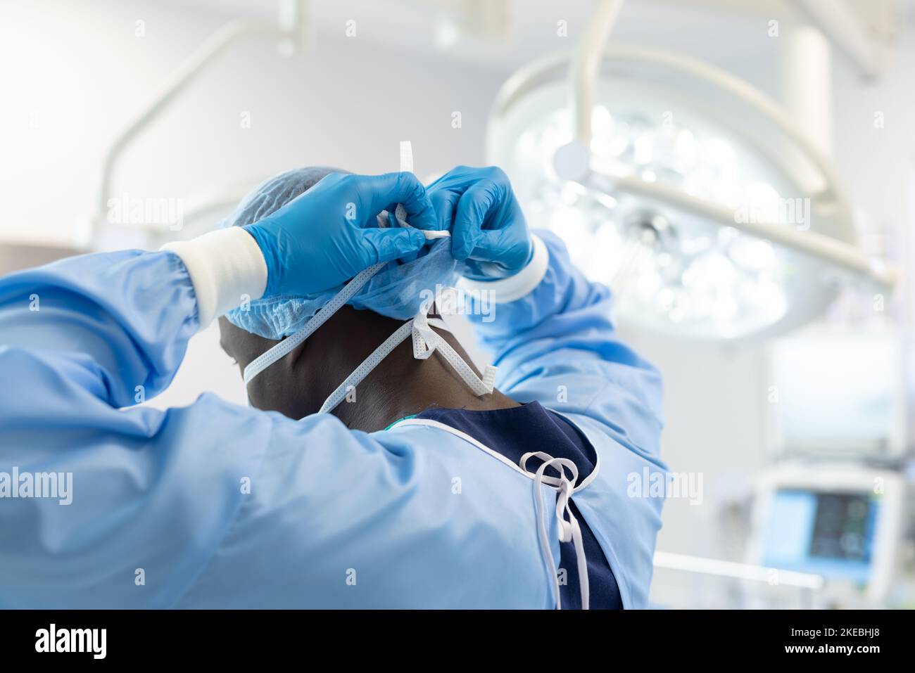 African american male surgeon in surgical gown and cap tying on mask in ...