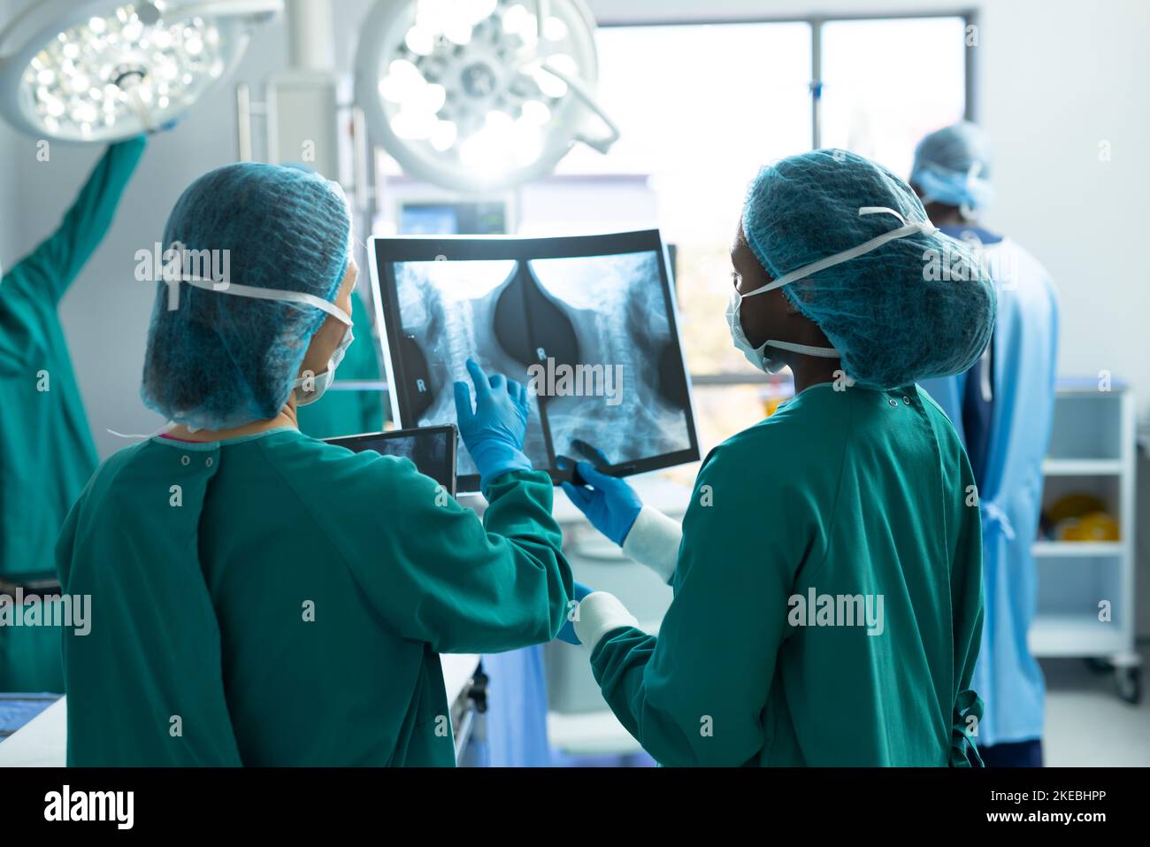 Rear view of two diverse female surgeons discussing x-ray in operating ...