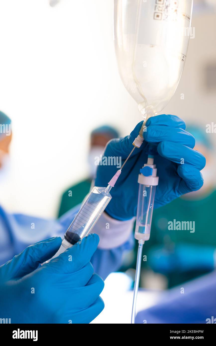 Vertical of gloved hand of surgical tech preparing iv bag in operating ...