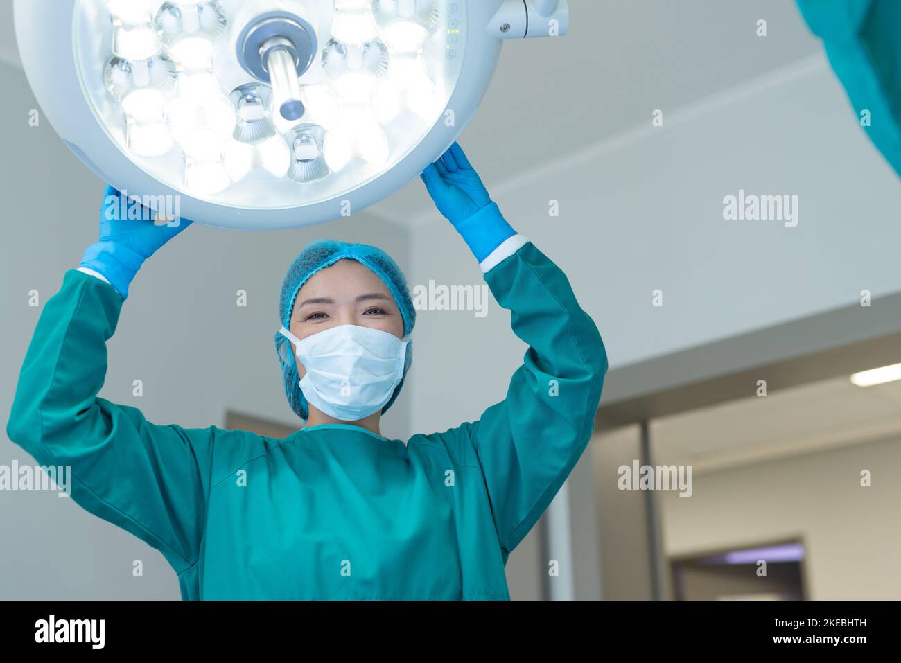 Smiling asian female surgeon adjusting lights in operating theatre for ...