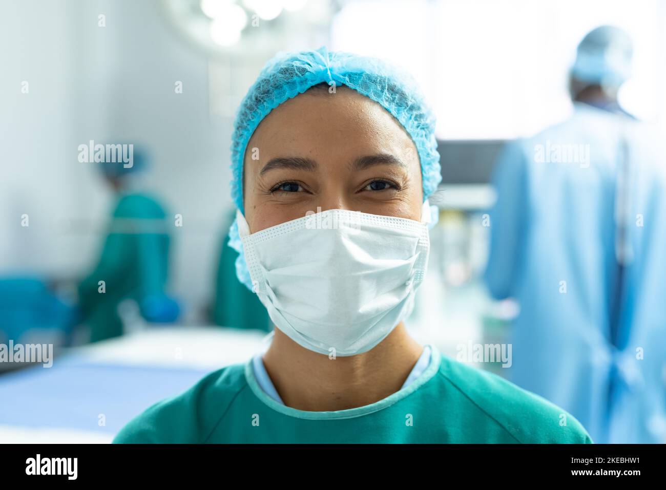 Portrait of smiling biracial female surgeon in surgical mask and cap in ...