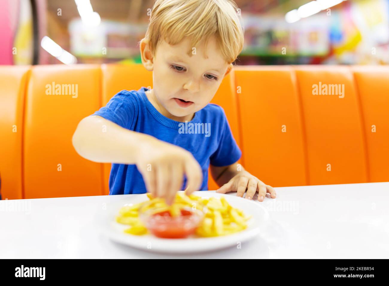 Cute child eating french fries with sauce at table in fast food ...