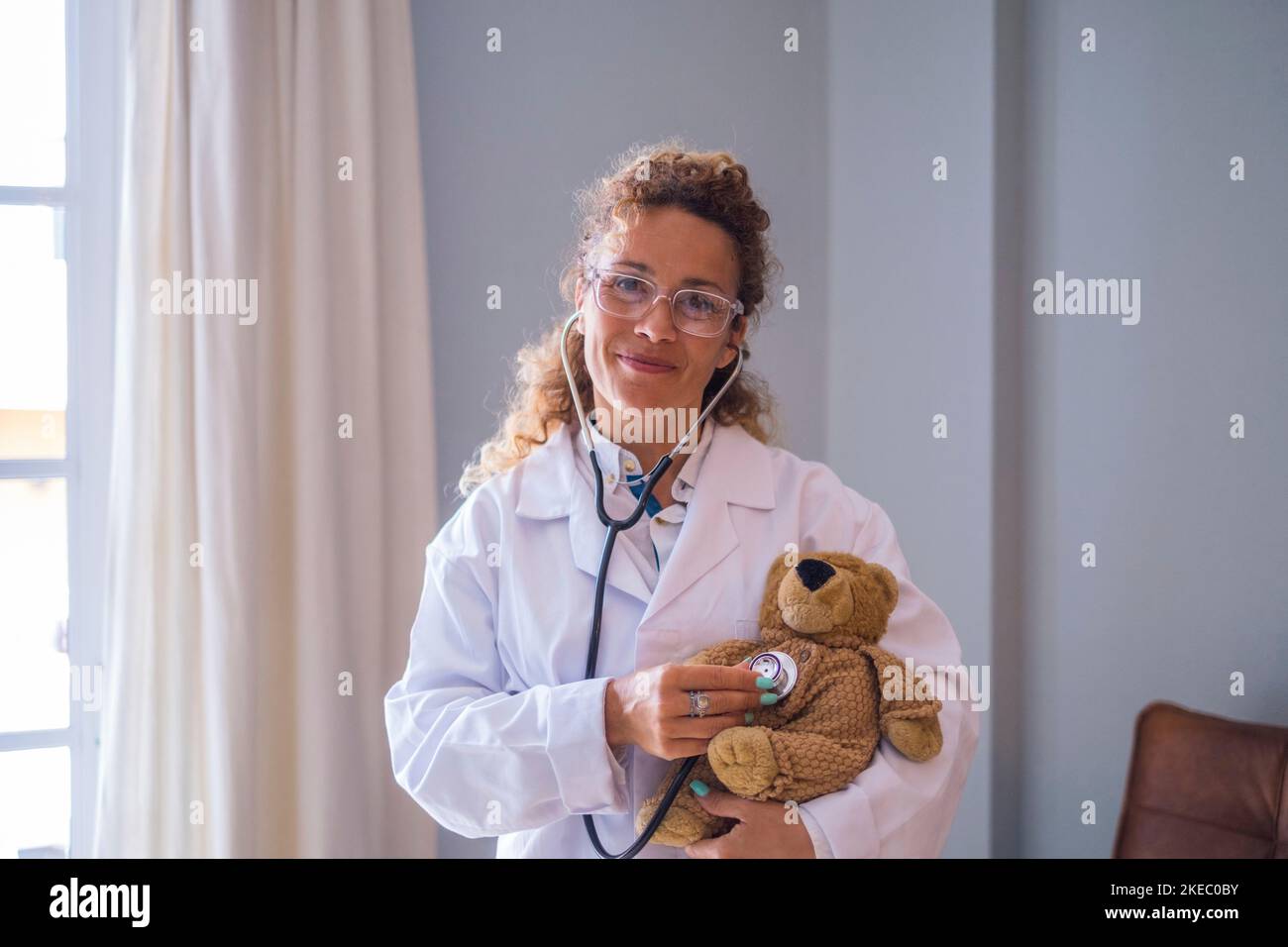 Portriat of young female doctor in uniform checking teddy bear with ...