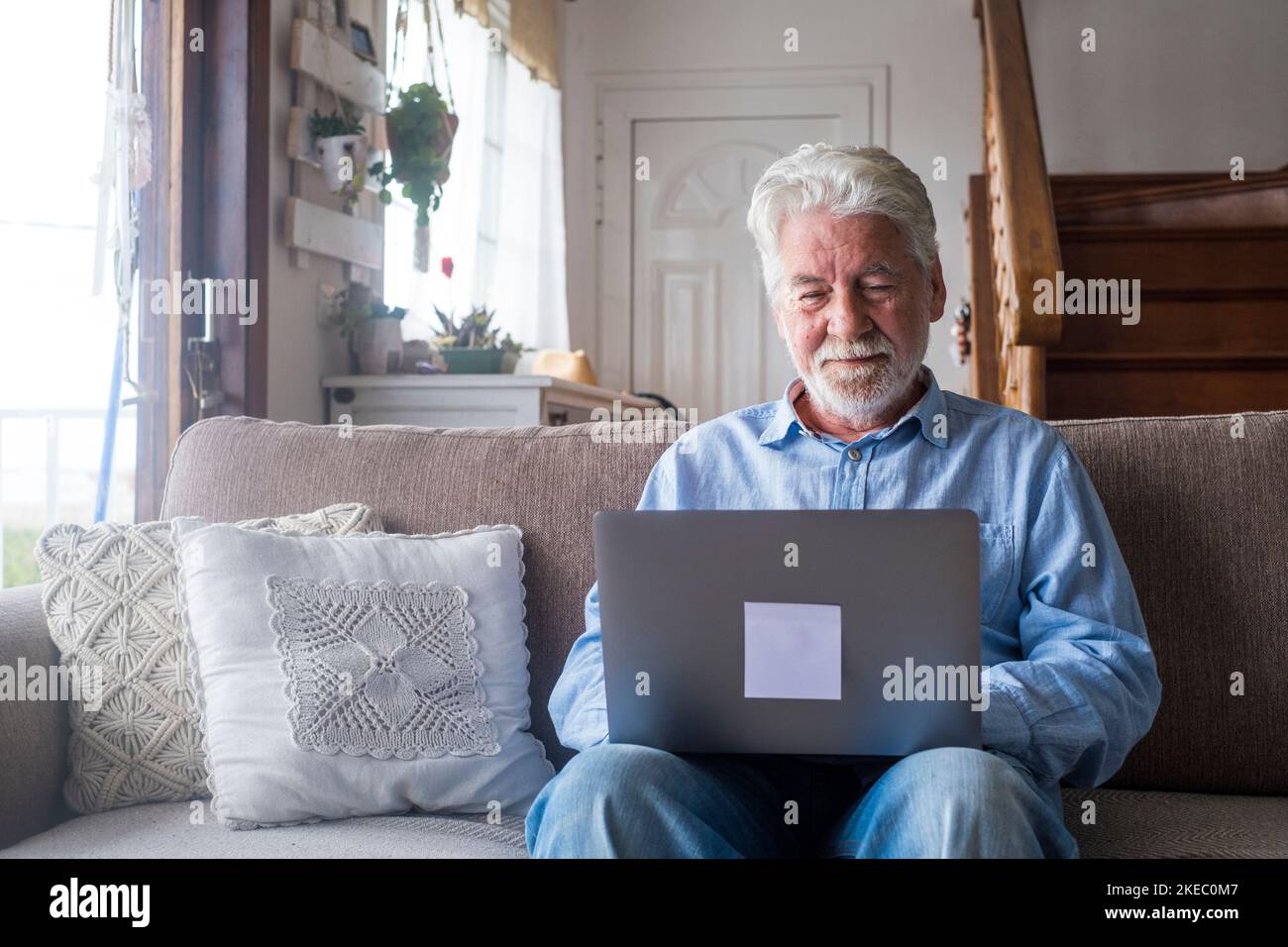 Old man using laptop with adhesive note on the back sitting on sofa in ...