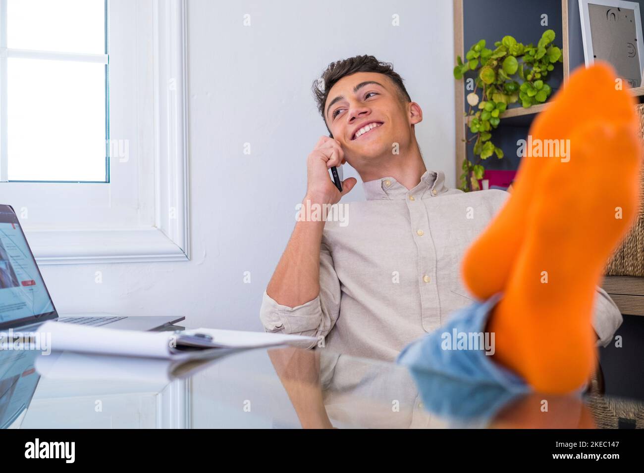 Satisfied teenager happy talking on phone at work with laptop in office ...