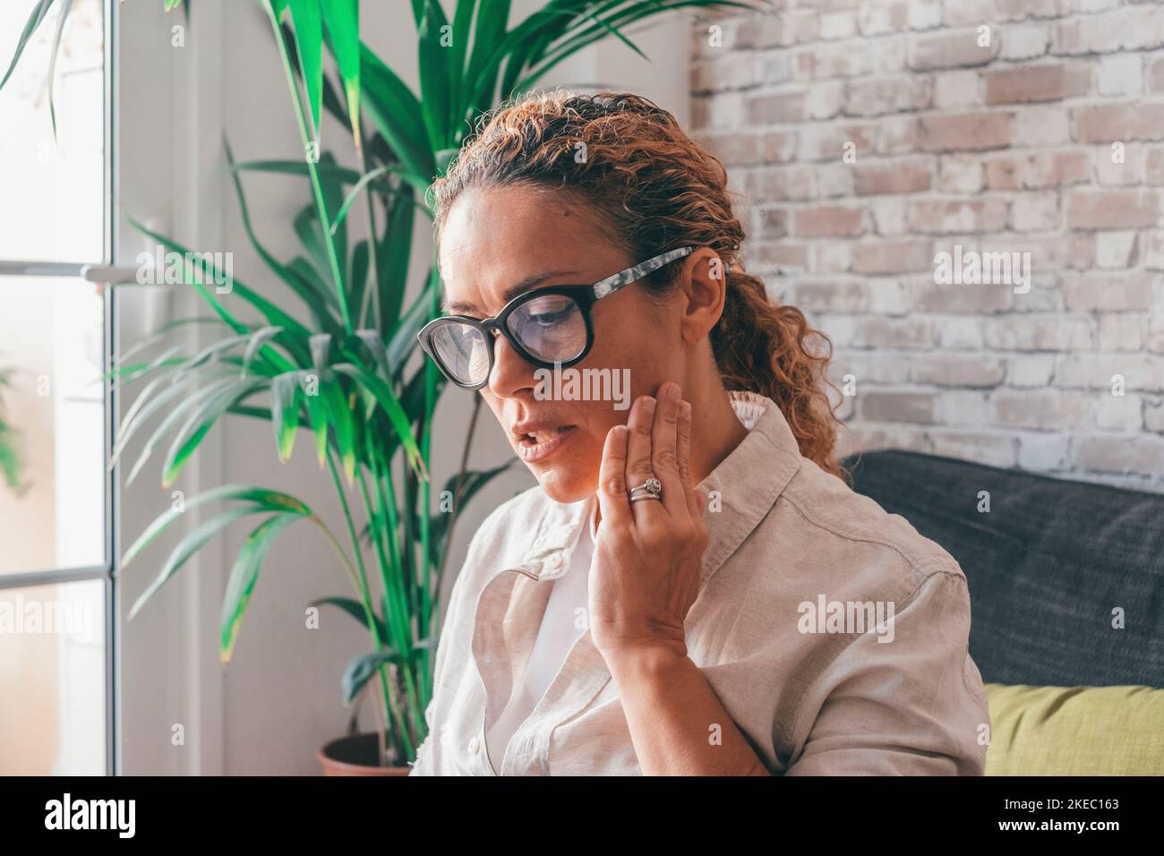Young woman suffering from tooth pain and touching cheek while sitting ...