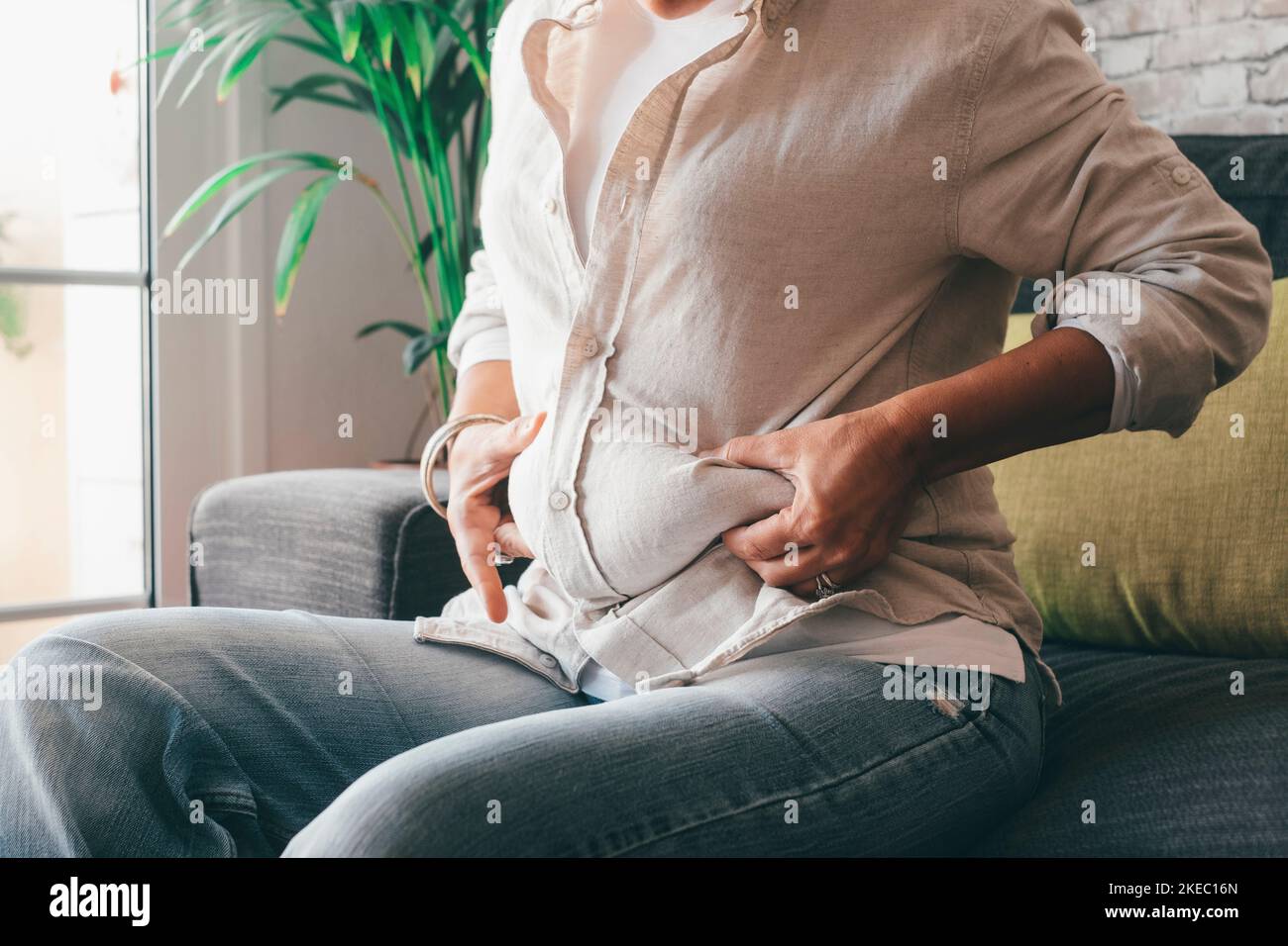 Midsection Of Woman Hands Holding Her Belly Fat Sitting On Sofa At Home