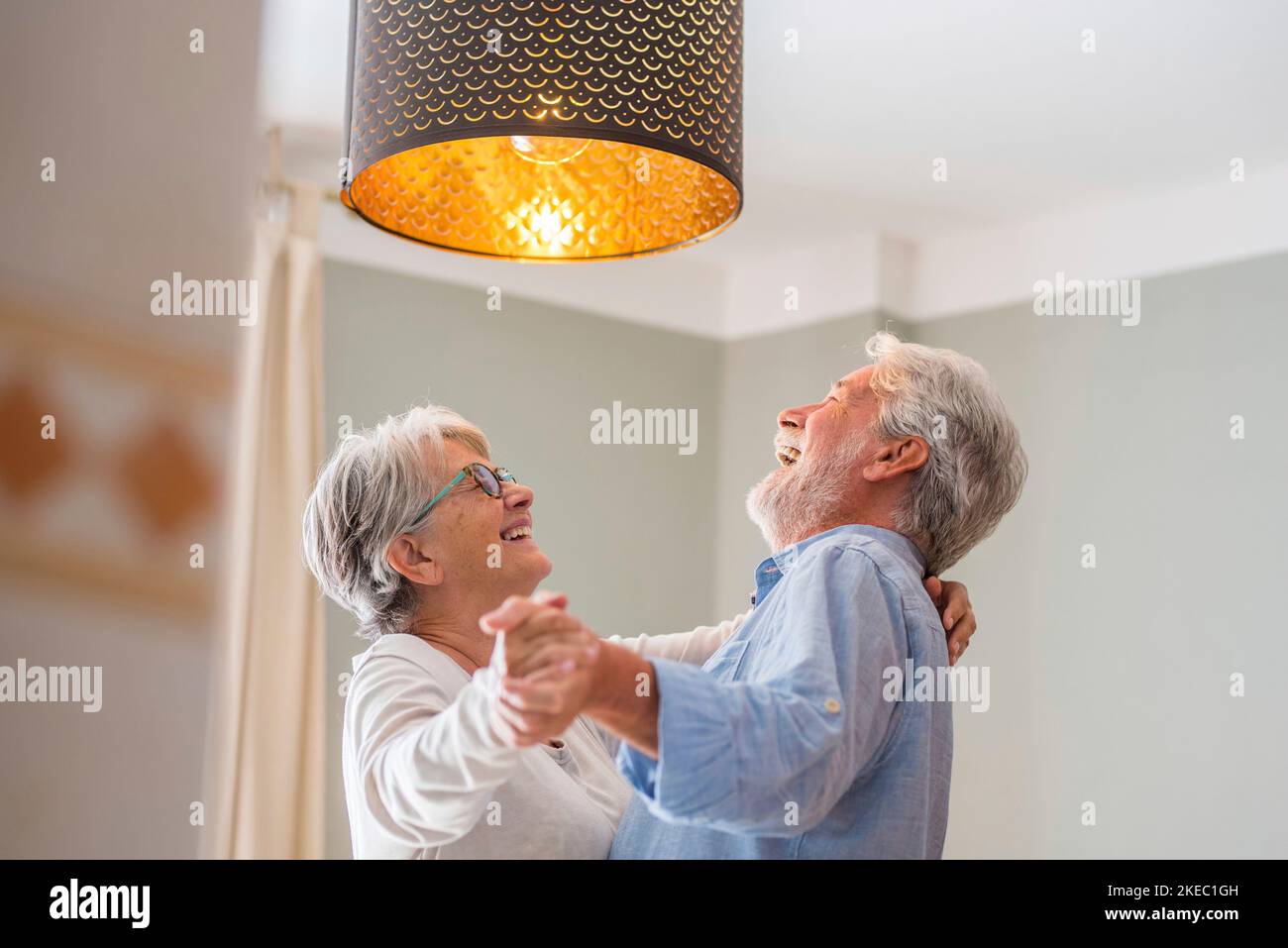 Cheerful senior couple dancing and laughing at home. Elderly happy couple celebrating by dancing ...