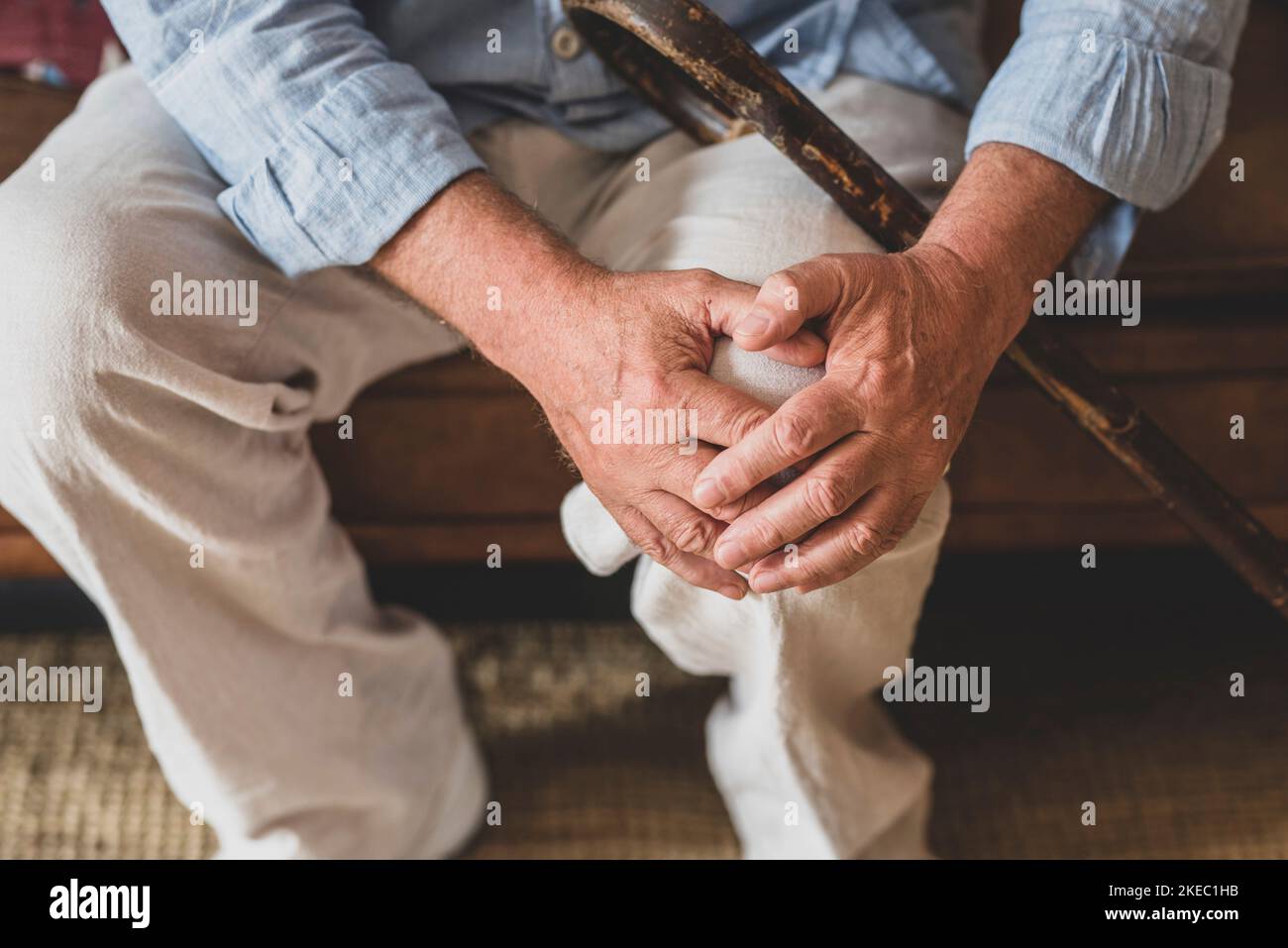 Close up of senior old man facing knee problem, sitting on sofa holding ...