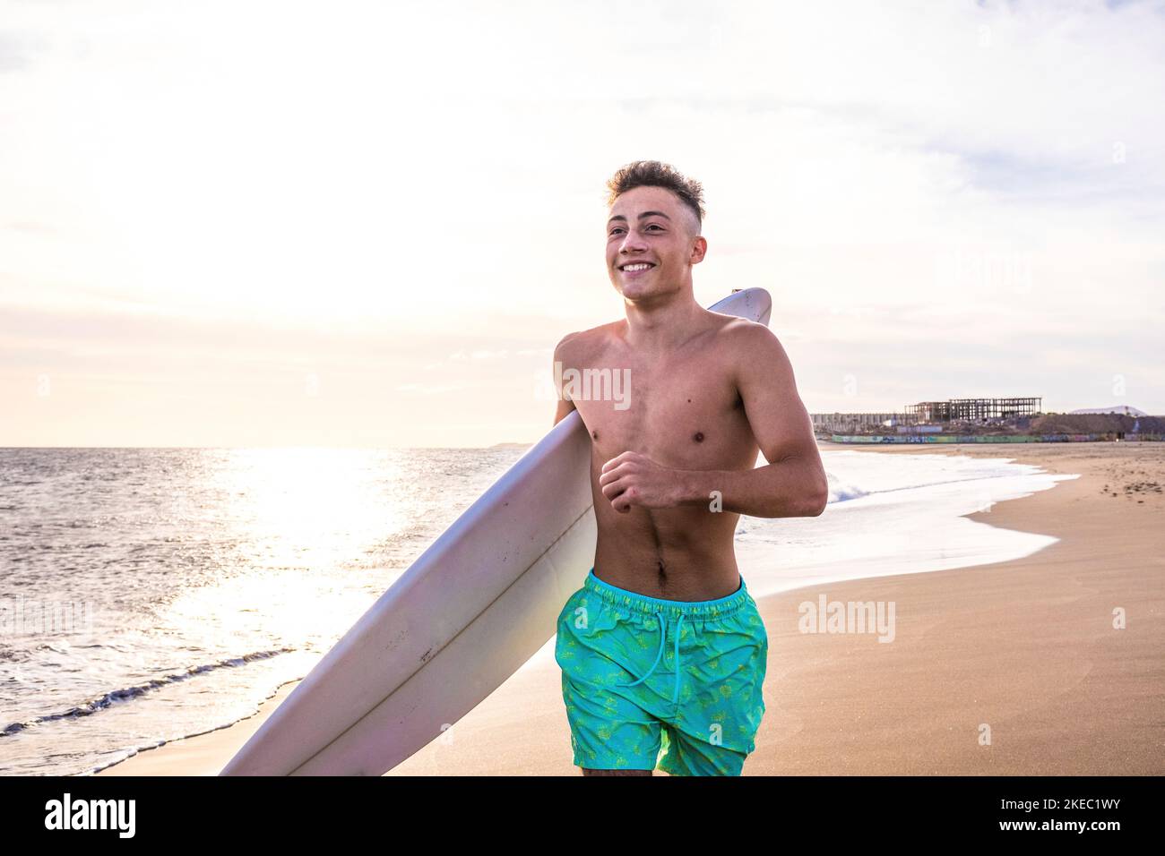 portrait of handsome young man walking on the beach with his surfboard ...