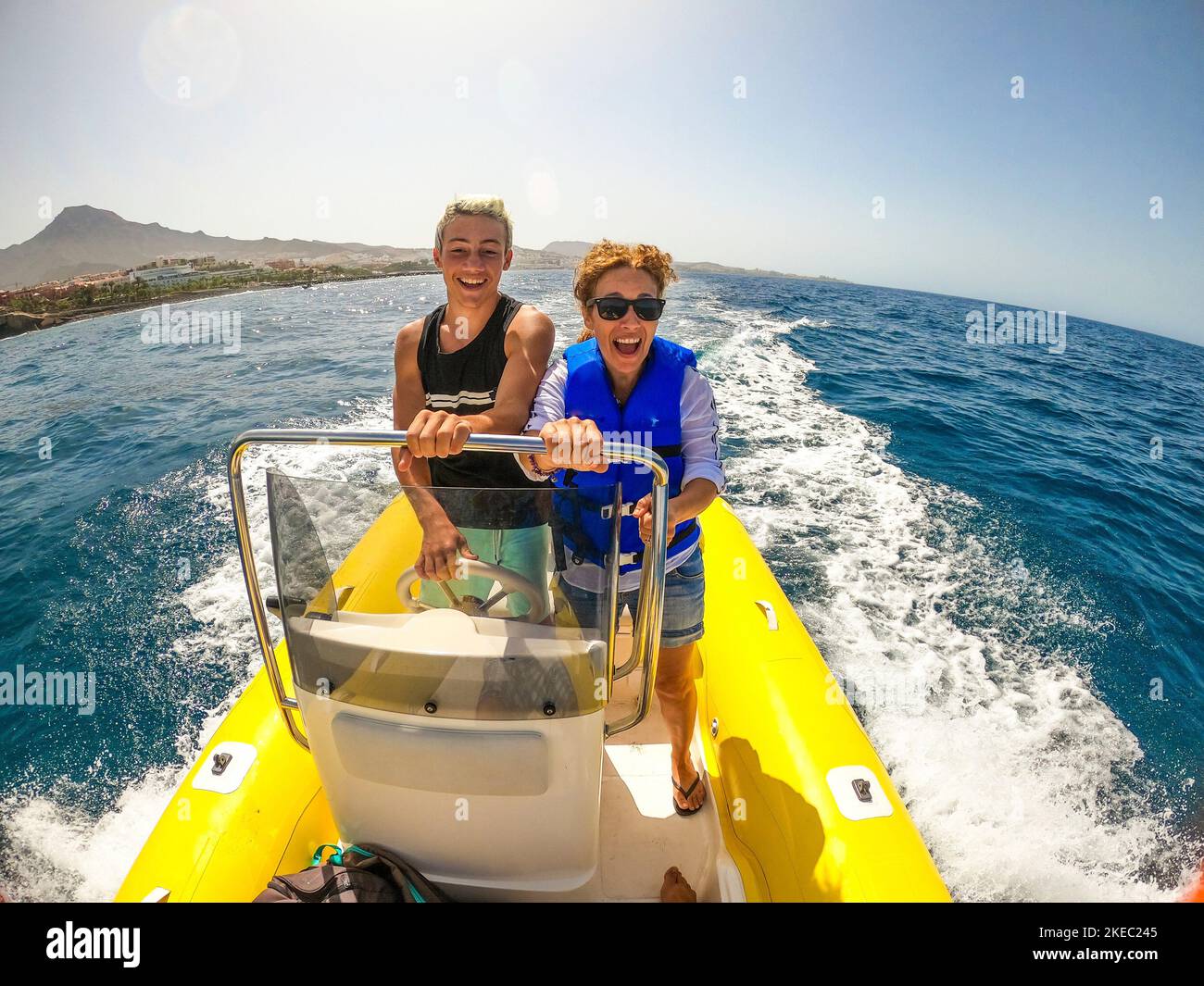 mom and son having fun and enjoying together in a boat drivig it and discovering the sea smiling ...