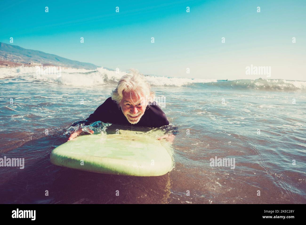 one senior trying surfing alone in the water of the beach and learning ...