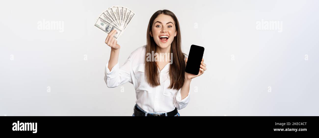 Enthusiastic young woman winning money, showing smartphone app ...