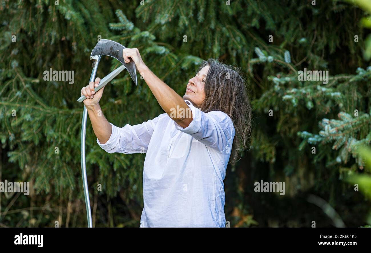 Woman cutting grass with scythe by hand, in garden, sharpening scythe ...