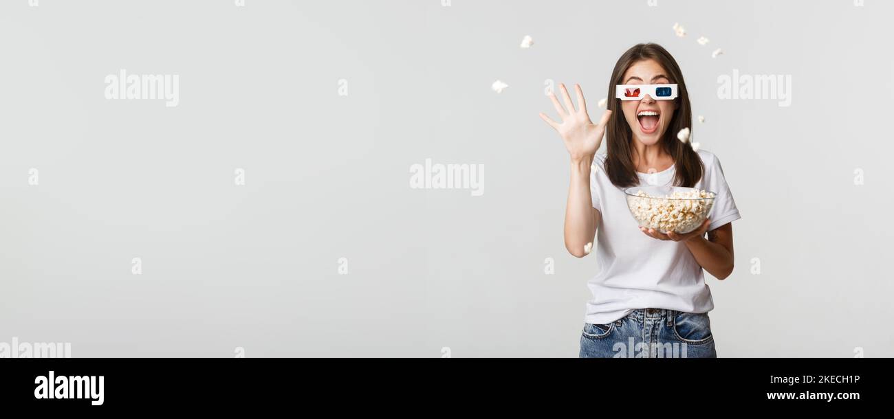 Joyful attractive young girl in 3d glasses, throwing popcorn at screen while watching movie ...