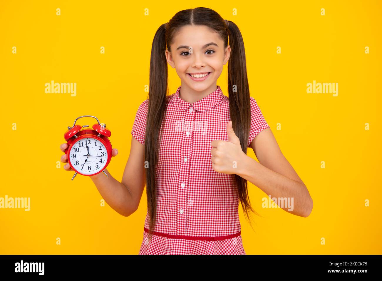 Happy teenager teen girl holding clock over yellow background. Early ...