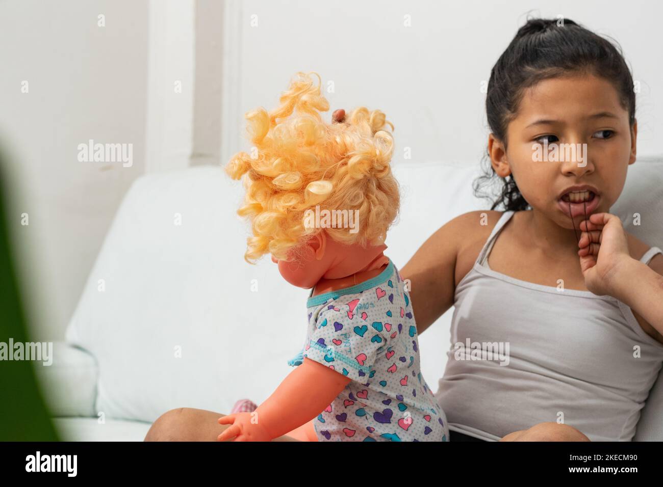 brunette girl combing her doll's hair while sitting on the living room ...