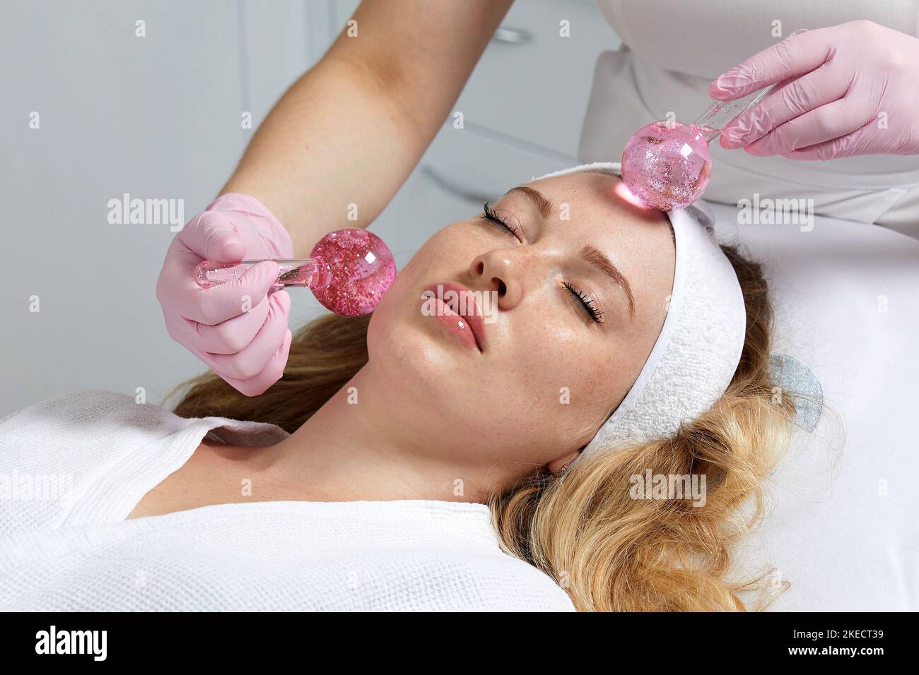 Young woman receiving facial massage with glass balls in beauty salon ...