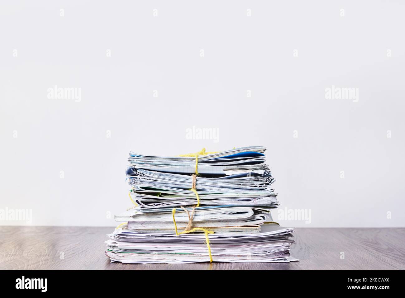 a stack of newspapers on a wooden table in front of a white wall, with ...