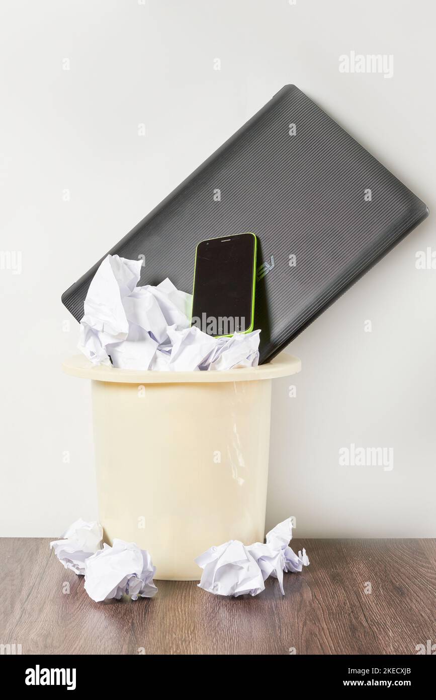 a cell phone in a trash can with crumpled paper on the floor next to it ...