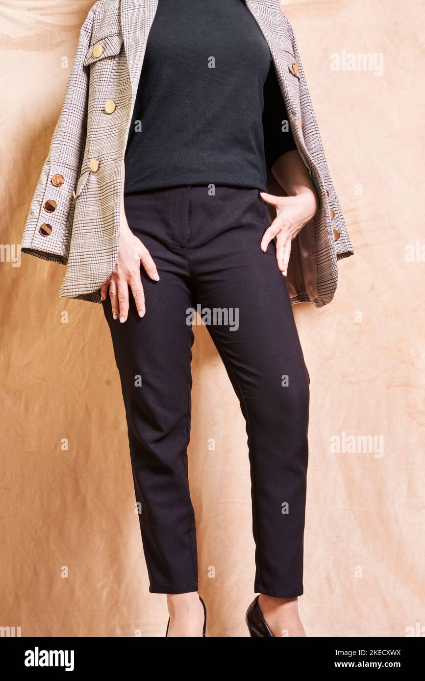 a woman in black pants and a blazer jacket, standing against a beige ...