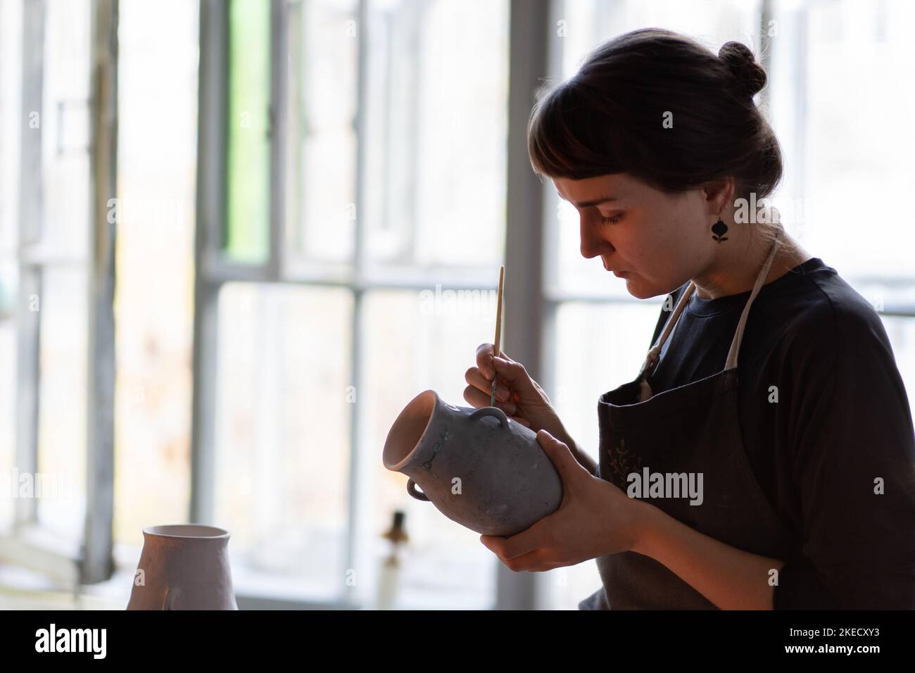 Emotionless woman brunette in apron works as artist in ceramist shop ...