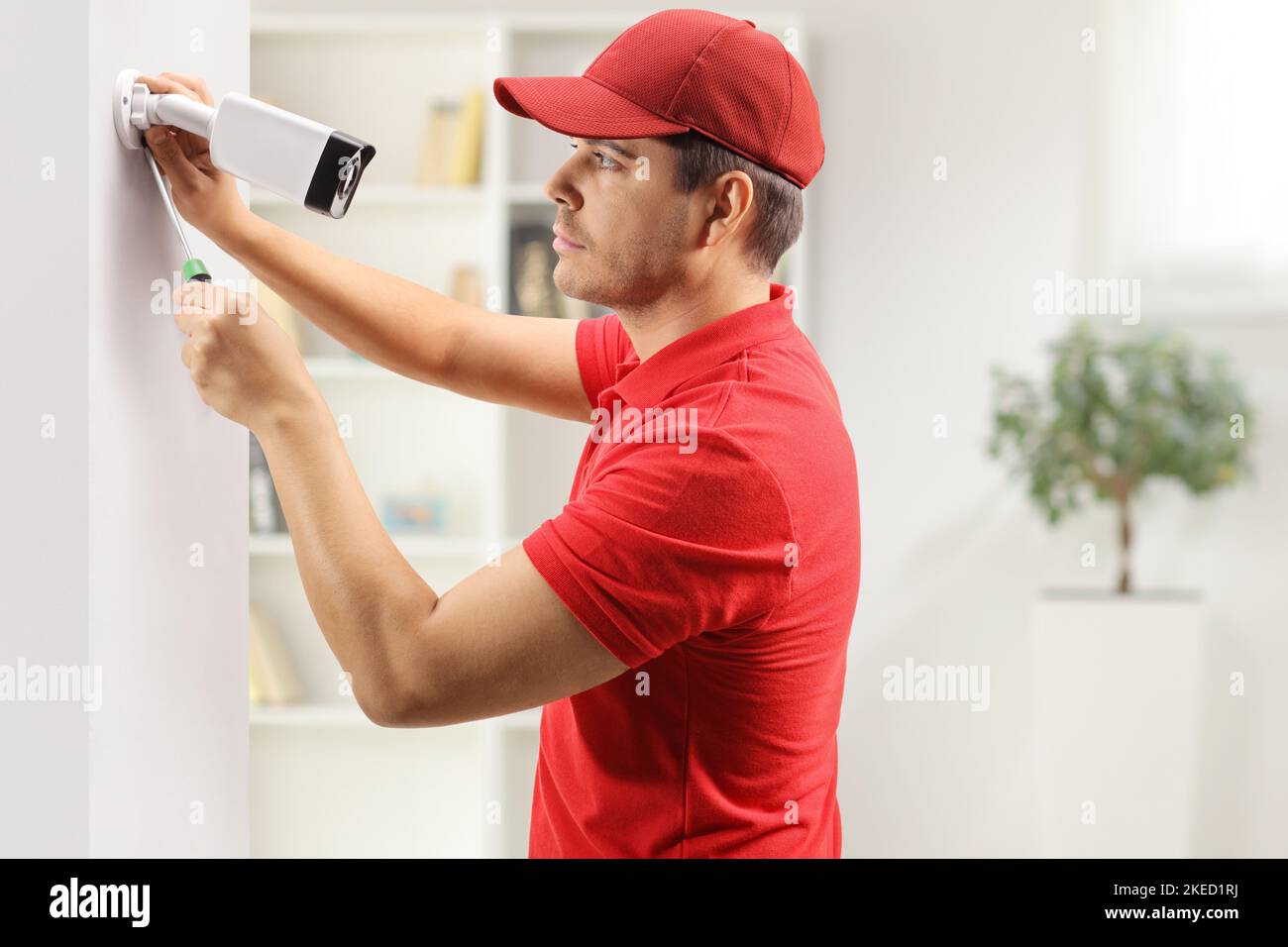 Profile shot of a young man installing a security camera on a wall in a ...