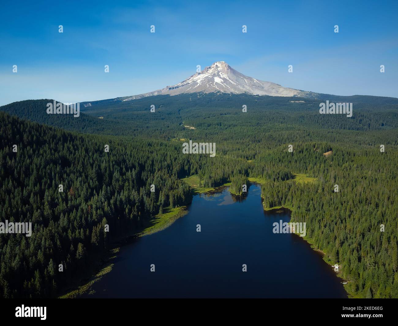 A green hilly meadow, a small dark blue lake, a snow-capped mountain, a ...