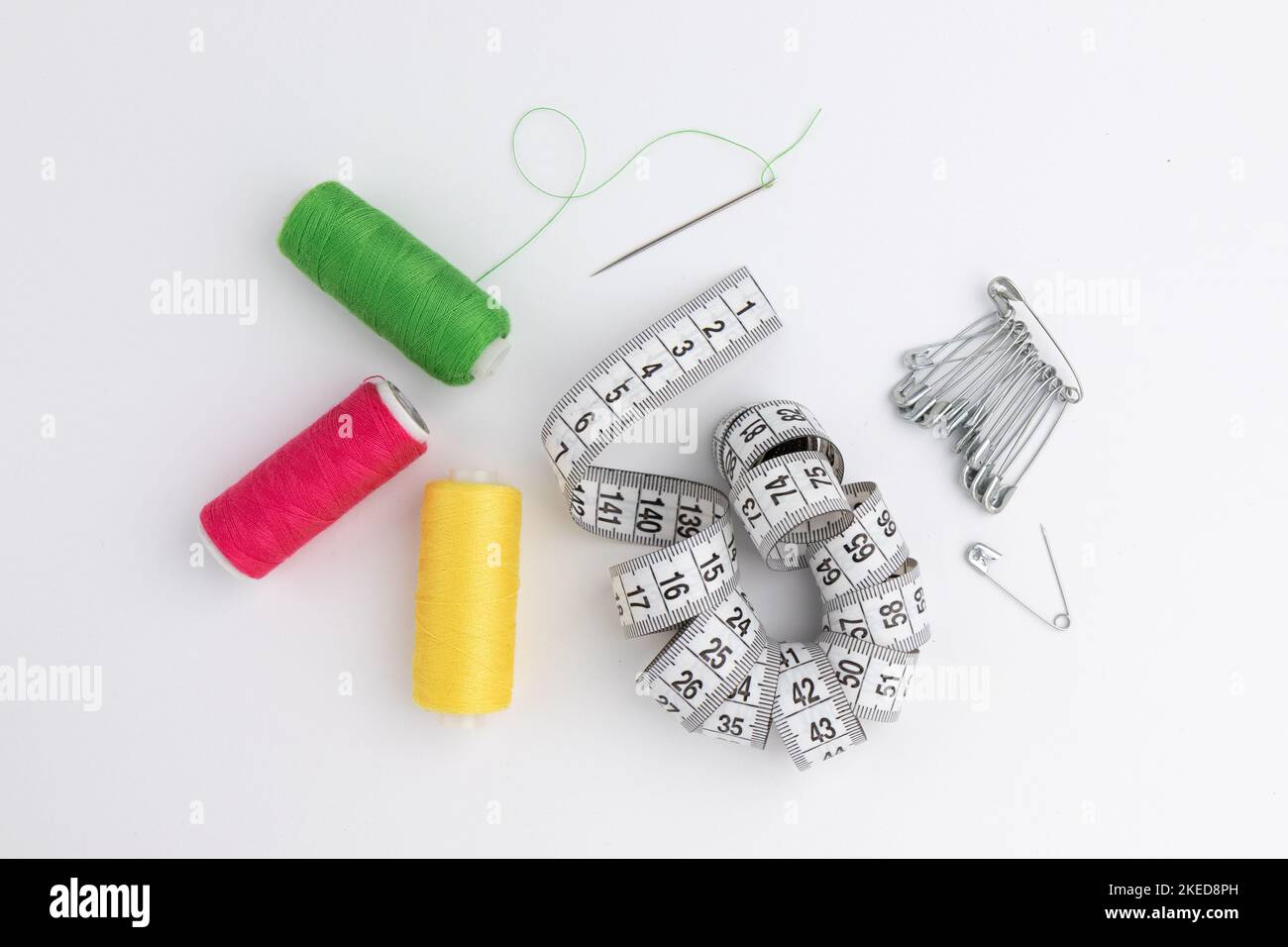 red, yellow and green thread coils, needle with thread, pins and tape ...