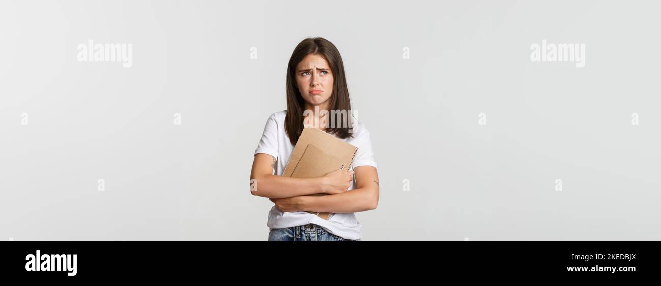 Portrait of sad and disappointed cute female student holding notebooks ...