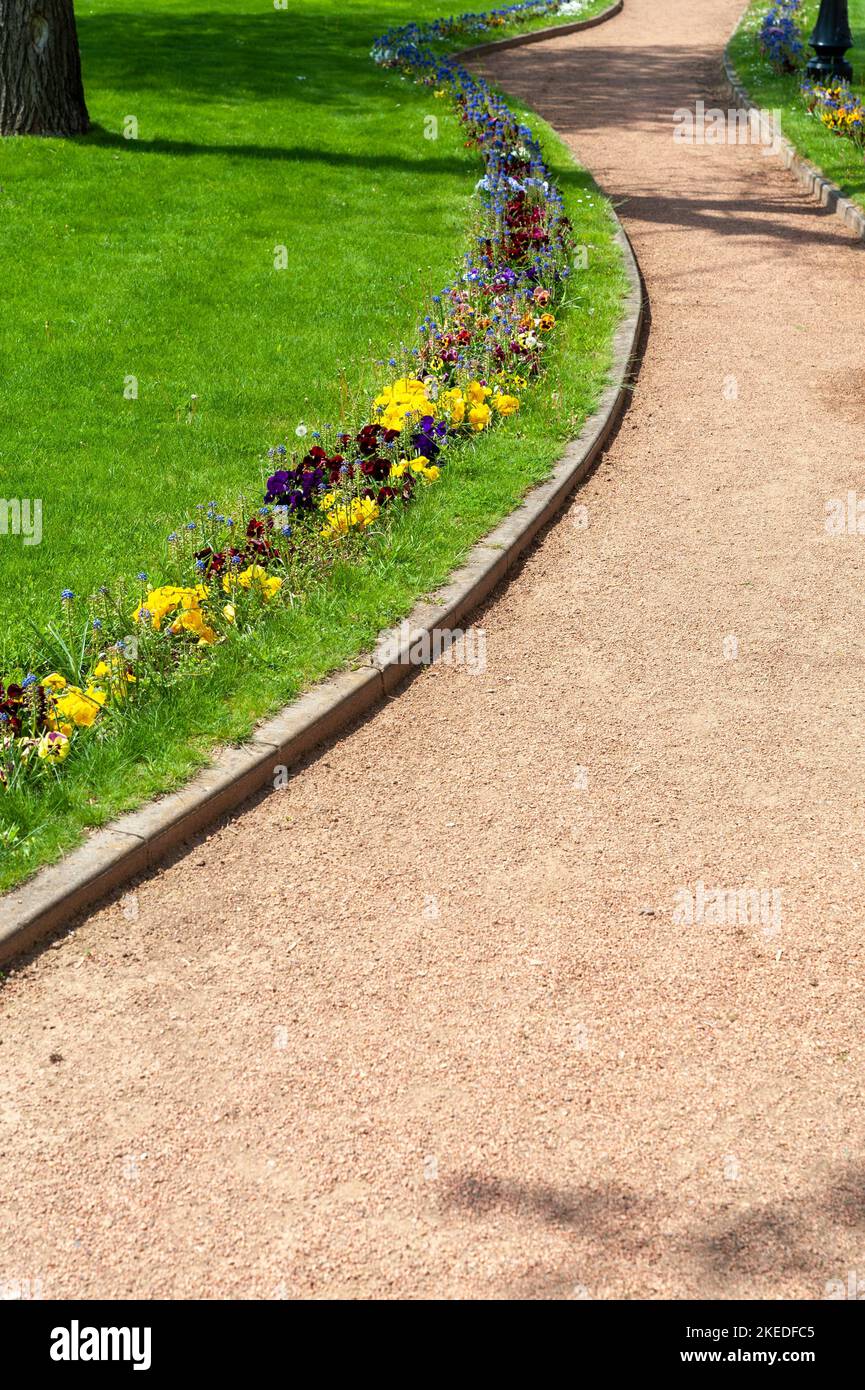 A vertical shot of a walking trail lined with small blooming flowers ...