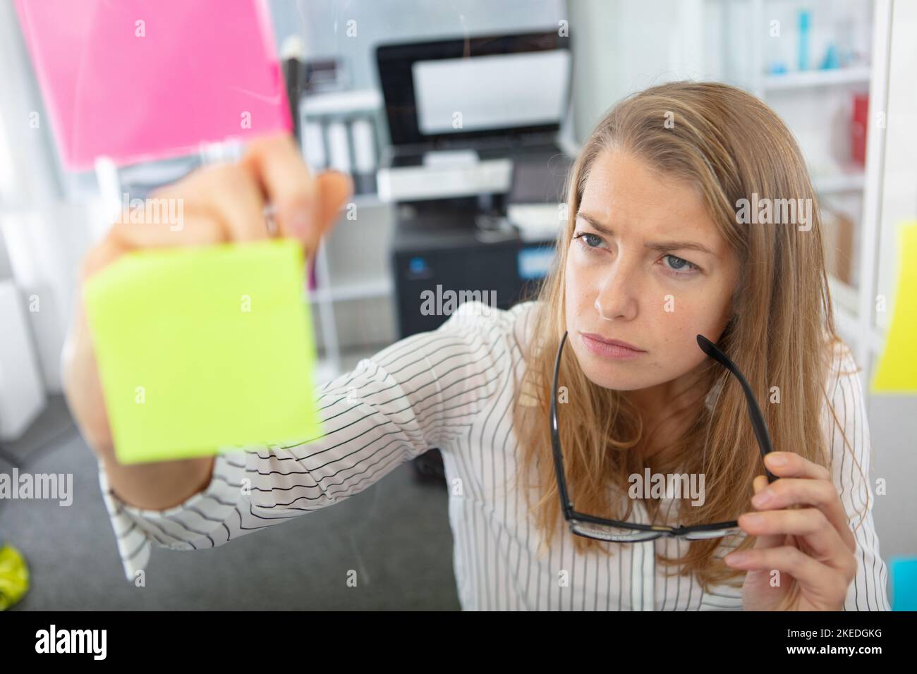 female worker frowning at sticky note on window Stock Photo - Alamy