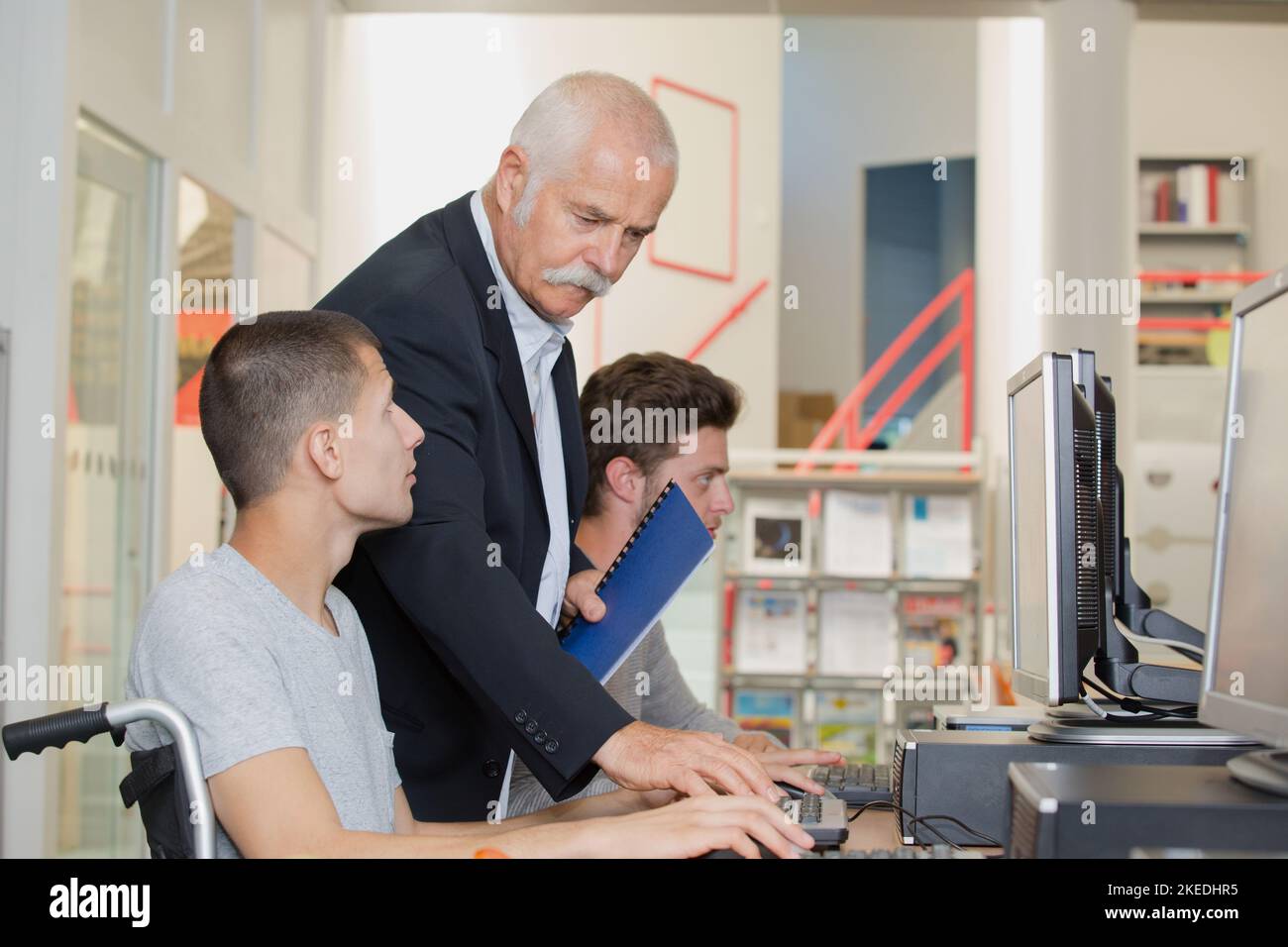 teacher helping young men using computers one in wheelchair Stock Photo ...